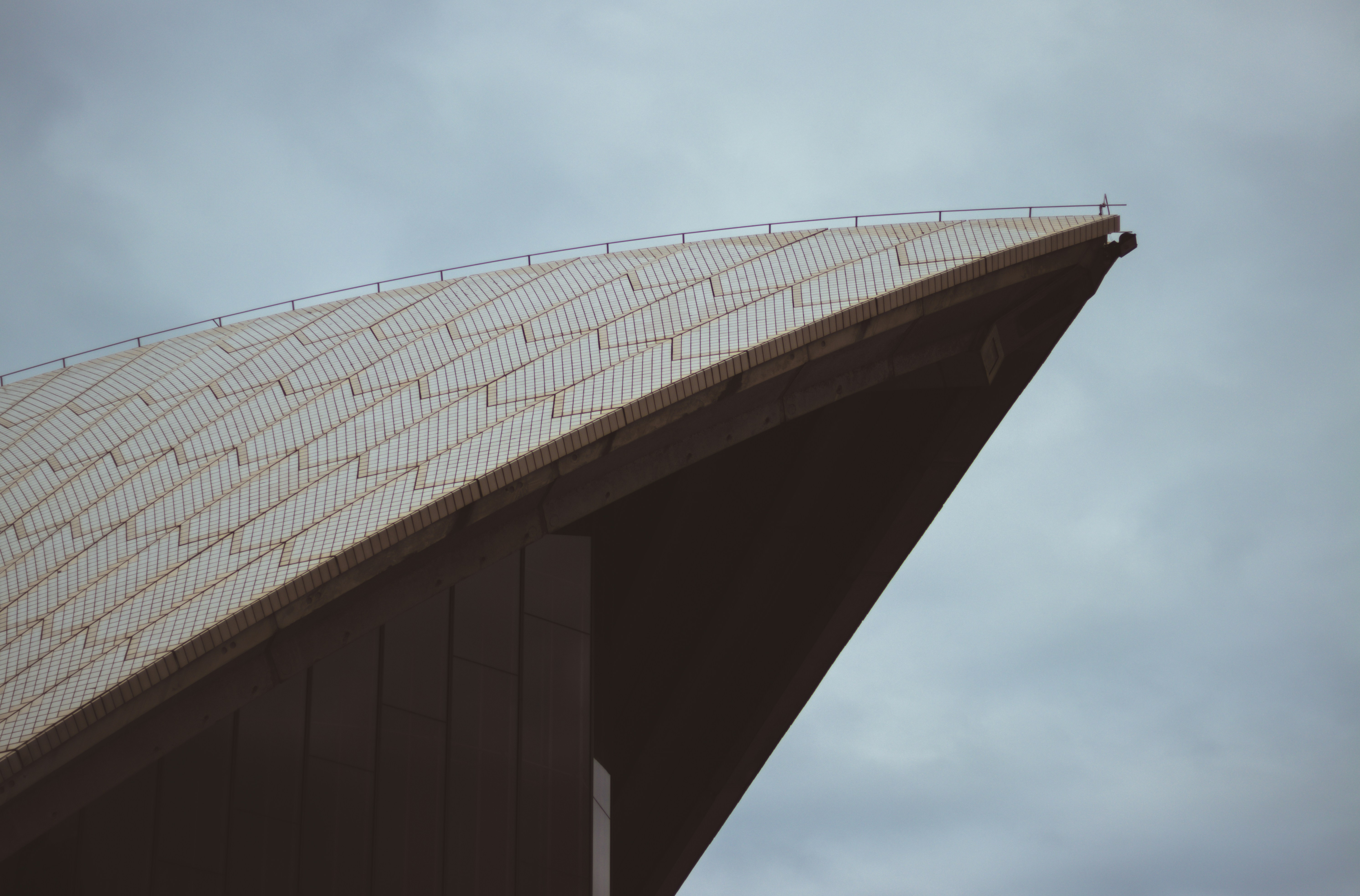 The distinctive roofline of a modern architectural structure under a cloudy sky, showcasing its sleek design and unique angles.