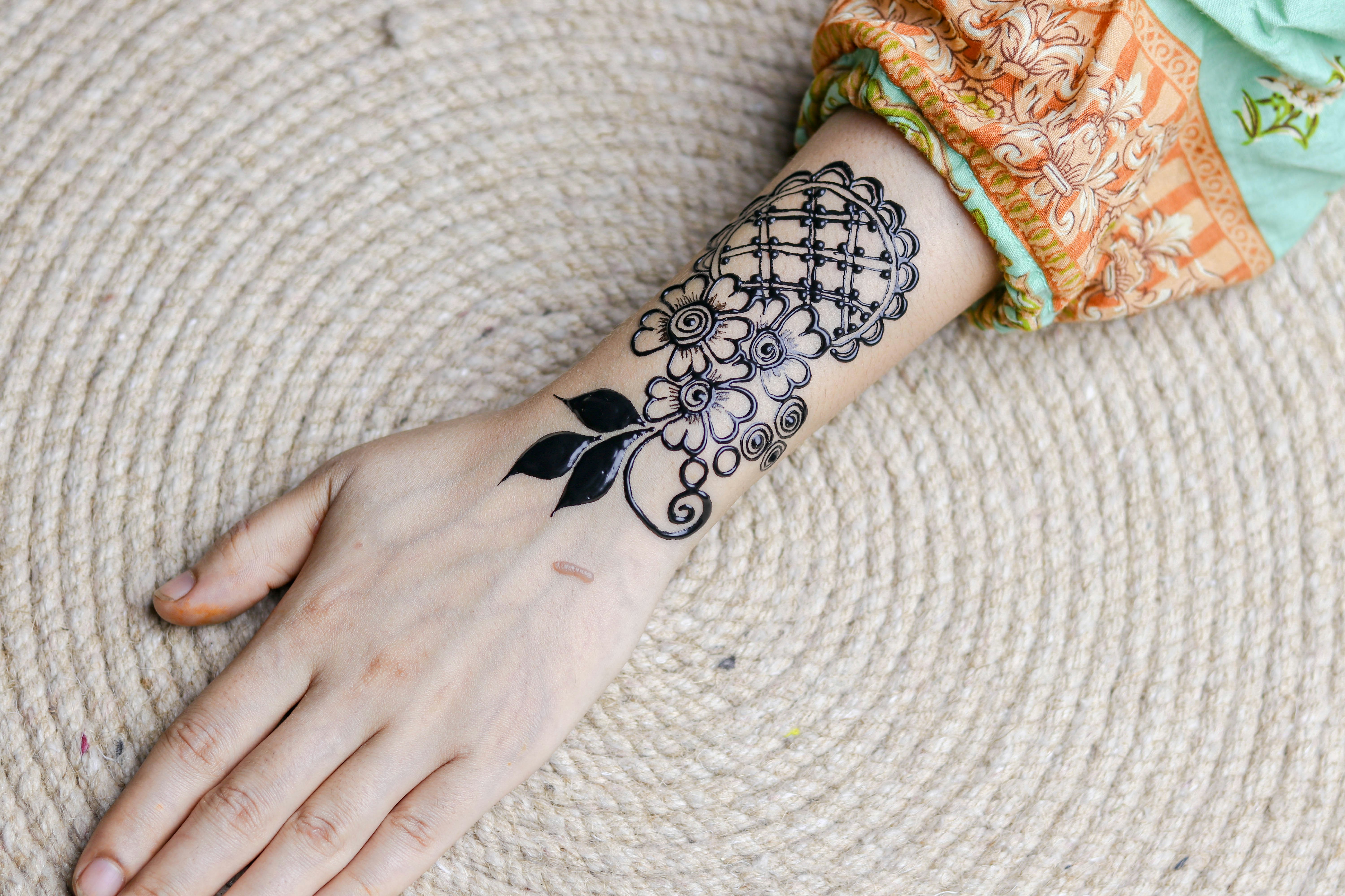 Detailed henna tattoo featuring floral designs and leaves on a wrist, showcasing the artistry of body art.