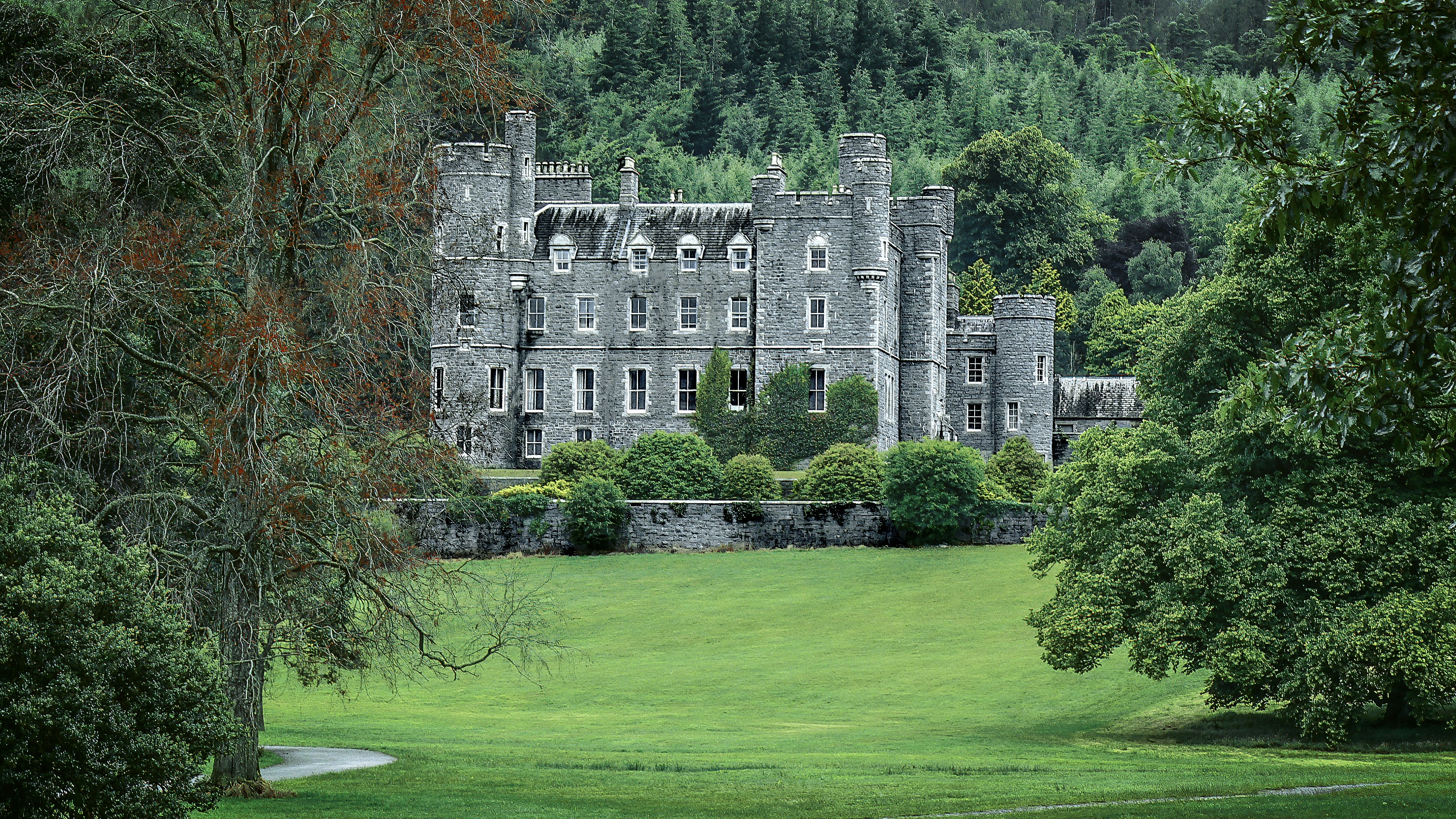 Medieval castle nestled among lush green trees and manicured lawns.