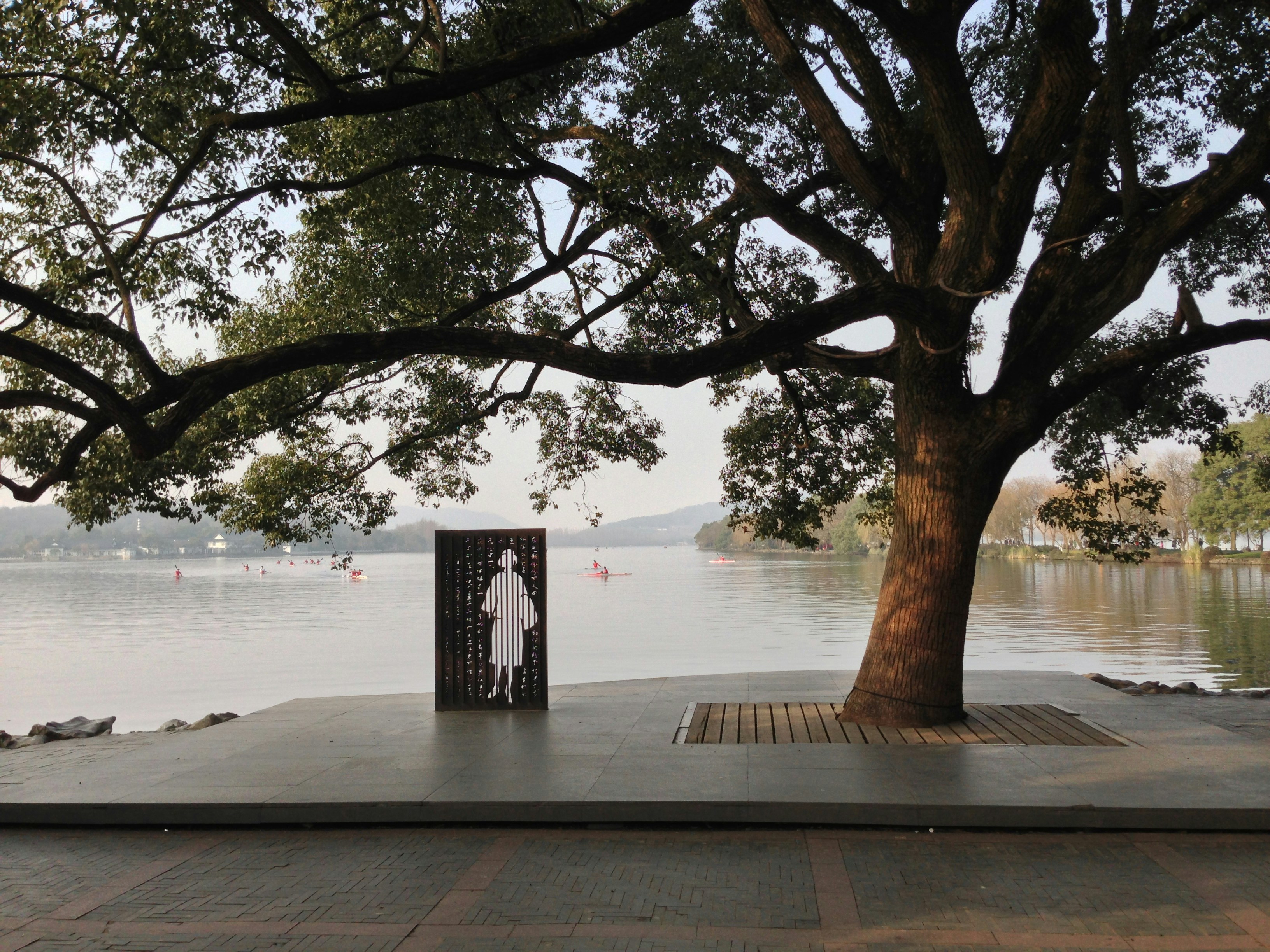 Artwork of a silhouetted figure beside a large tree overlooking a placid lake on a clear day.