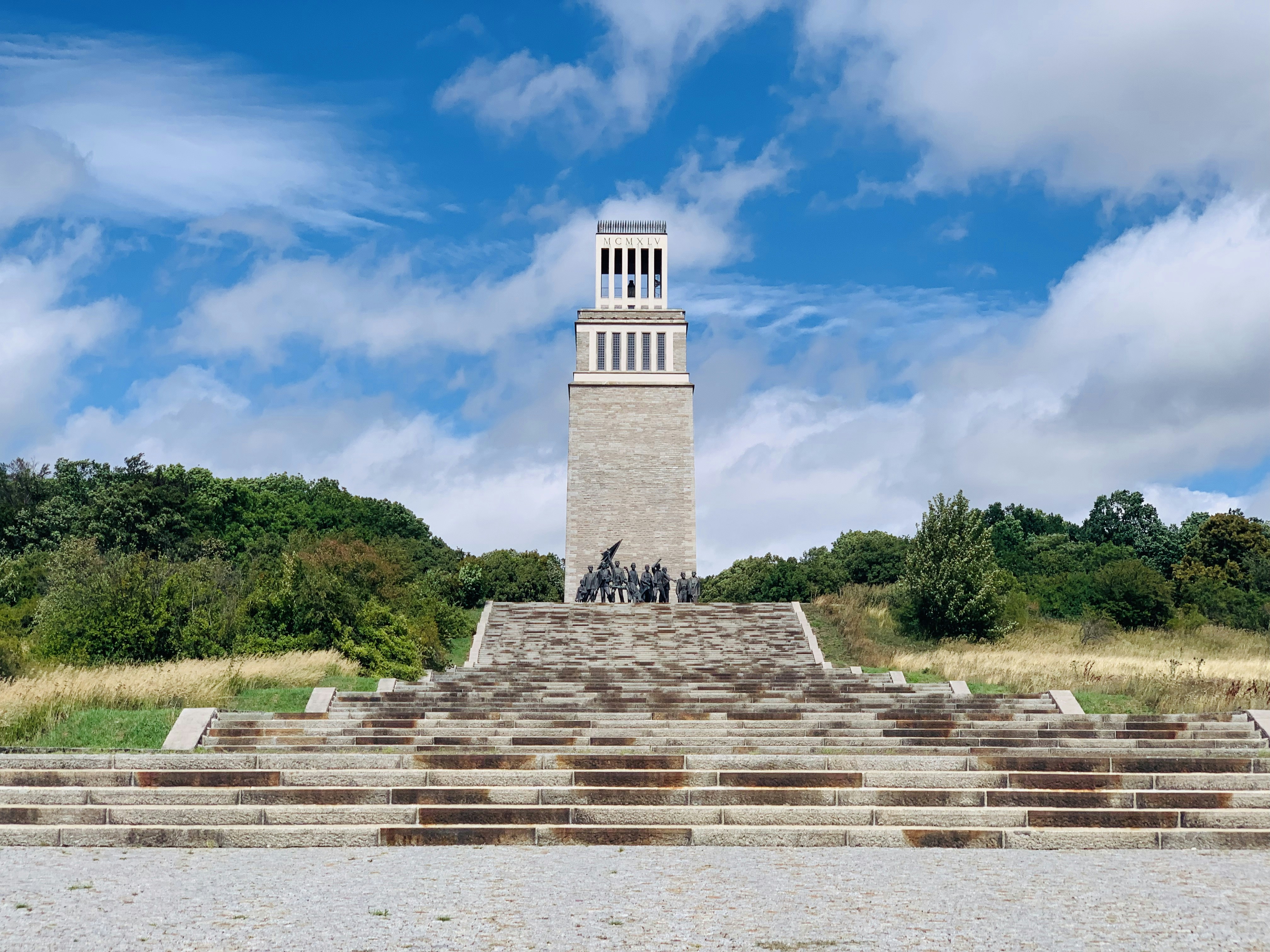 Stone steps leading to a tall, rectangular tower against a vivid blue sky with scattered clouds.