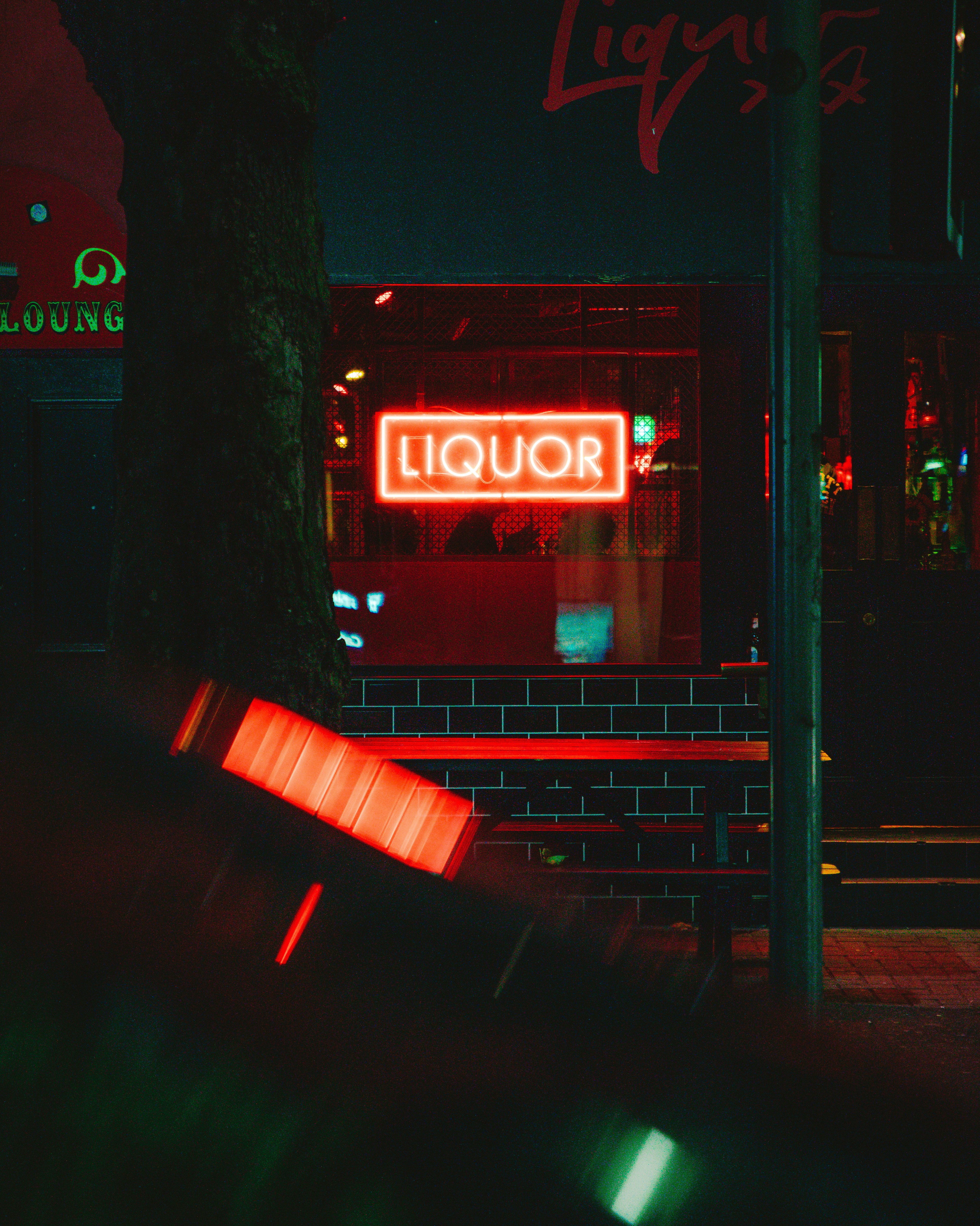 Bright neon 'LIQUOR' sign illuminating a bar entrance, with reflections hinting at the vibrant atmosphere inside.