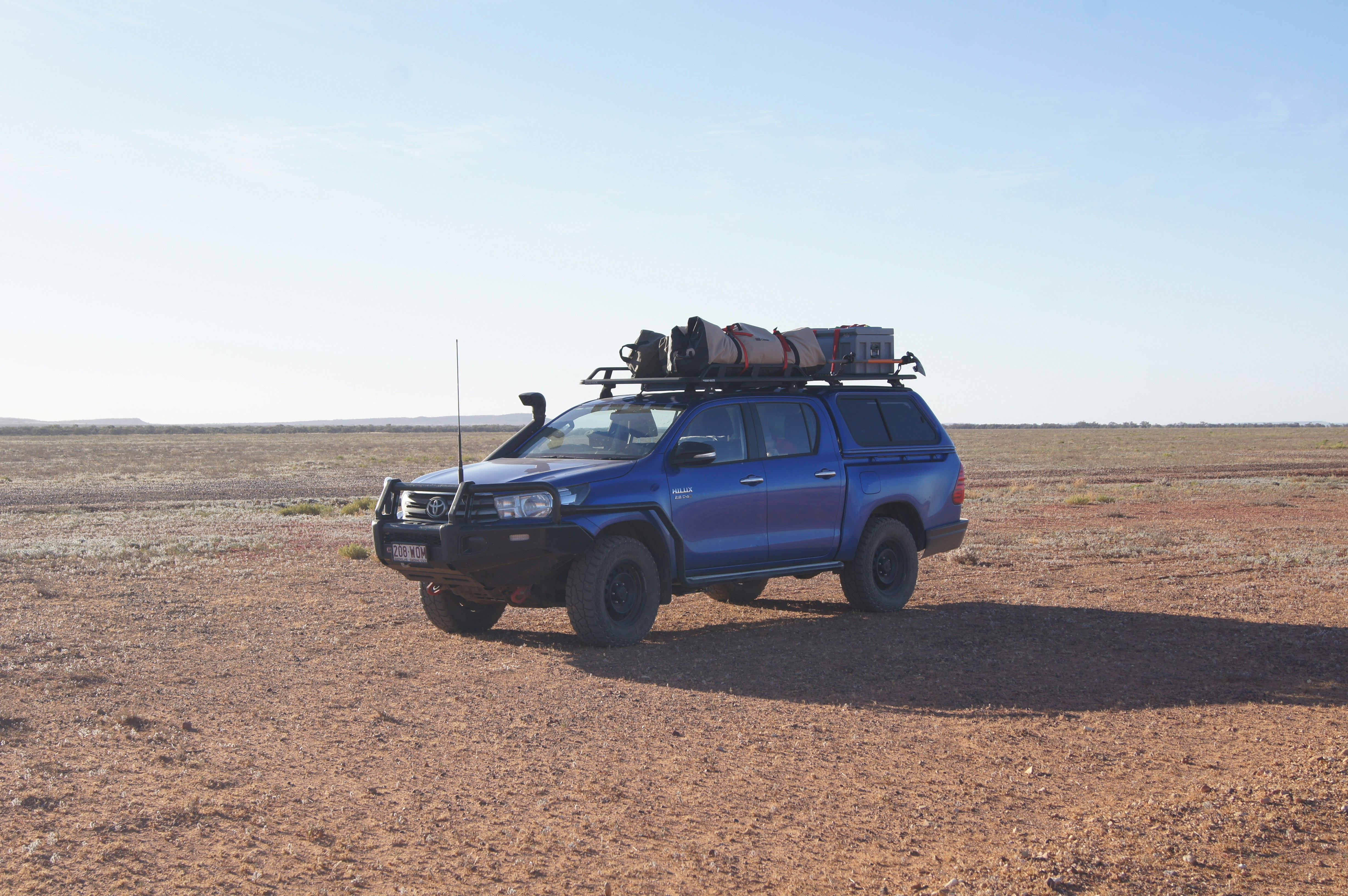 Blue SUV equipped for adventure parked on a vast, sunlit desert plain.