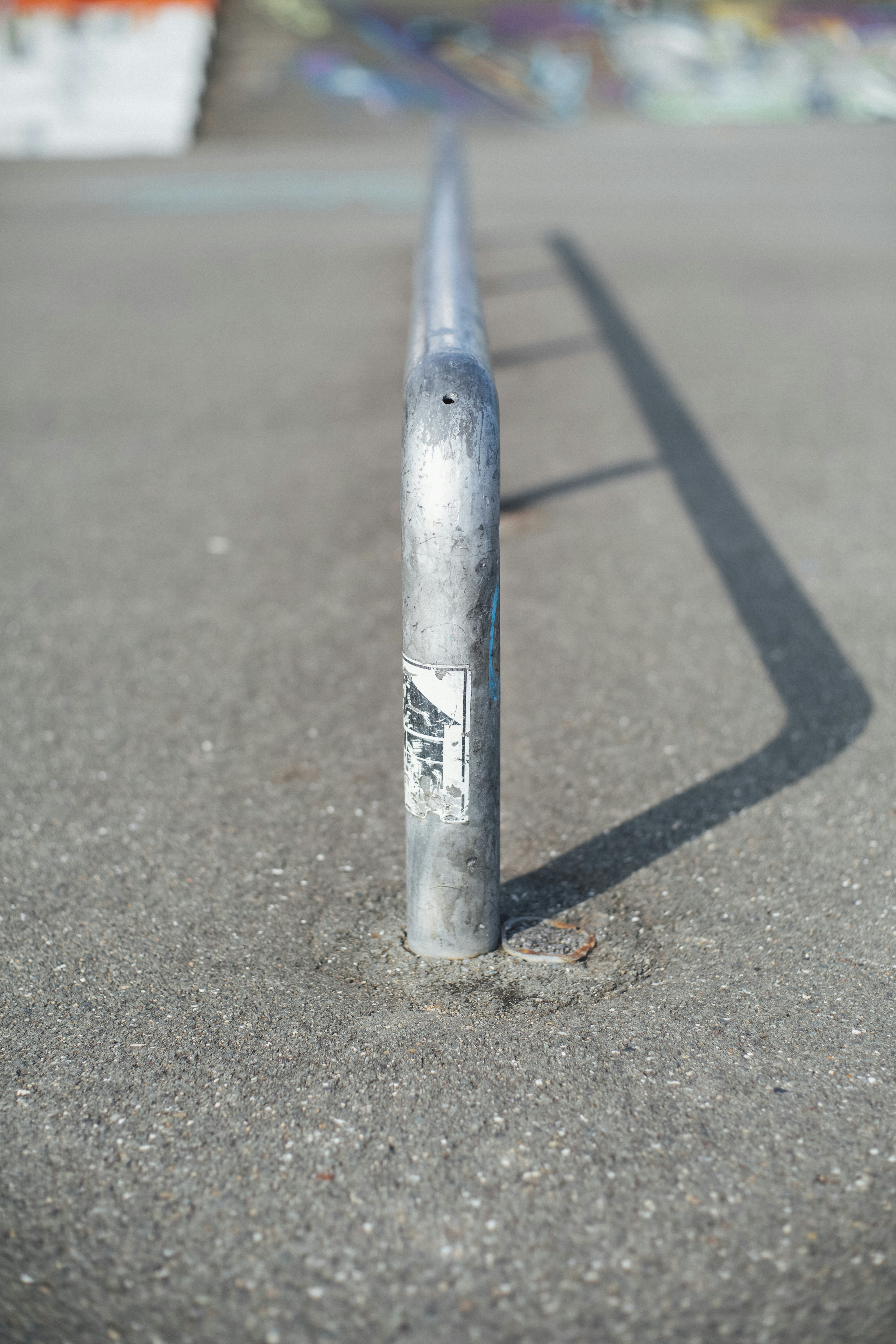 Close-up of a metal rail embedded in concrete, casting a long shadow on the ground. The scene captures the essence of urban skate culture.