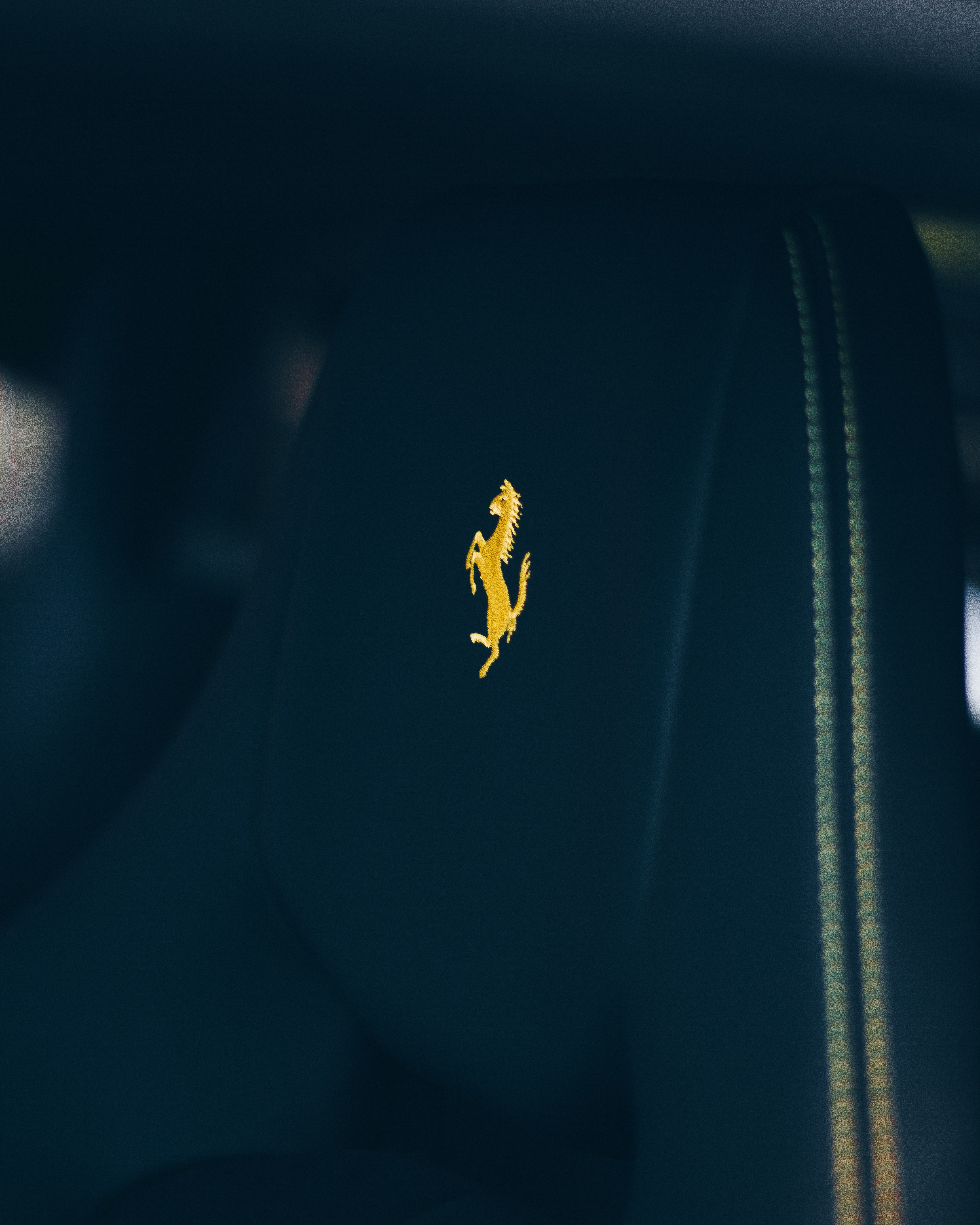 Close-up of a Ferrari seat featuring the iconic prancing horse logo in gold against a sleek black background.