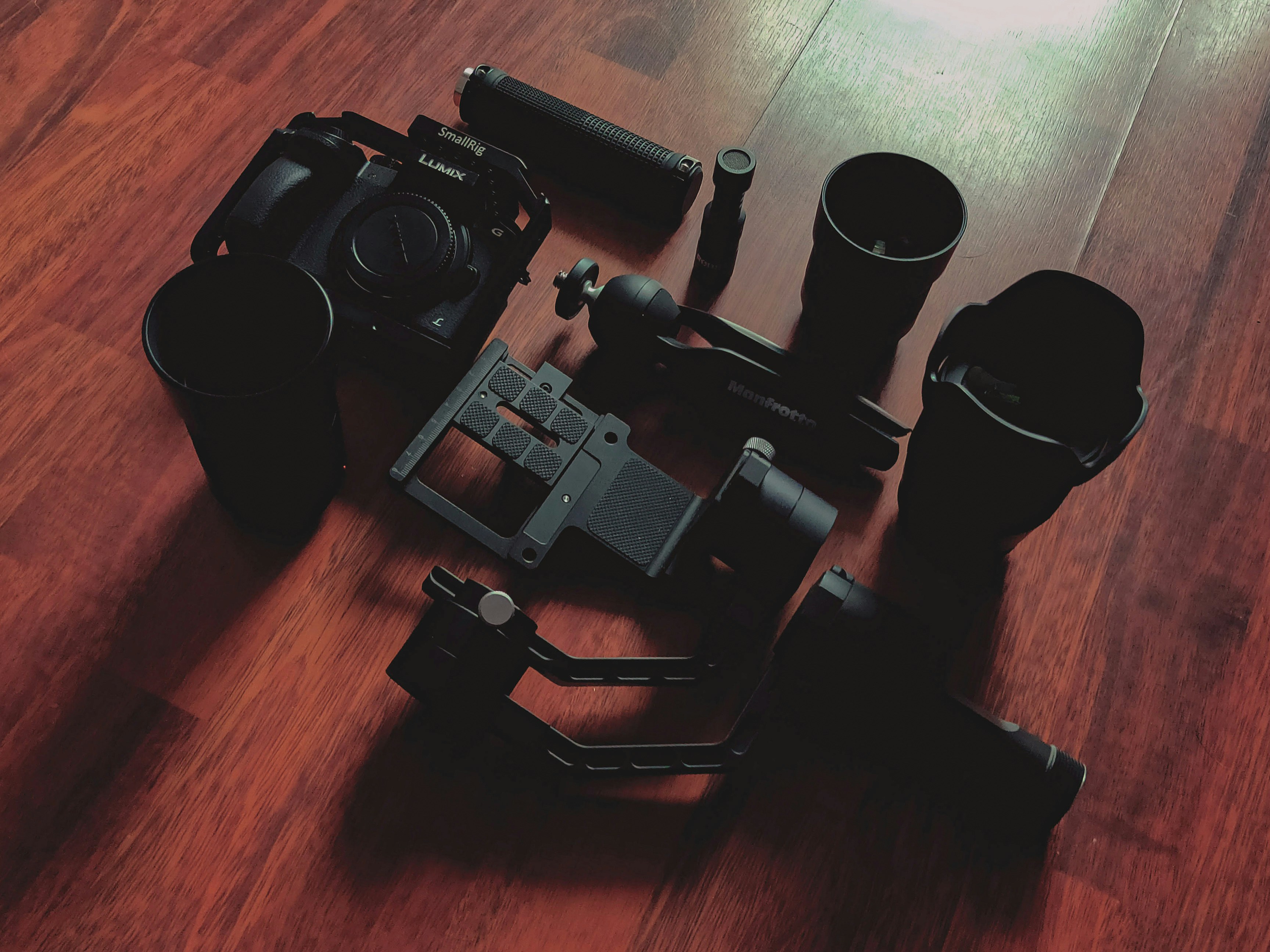 A collection of camera accessories and a Panasonic Lumix camera arranged on a wooden surface, showcasing the tools of photography.
