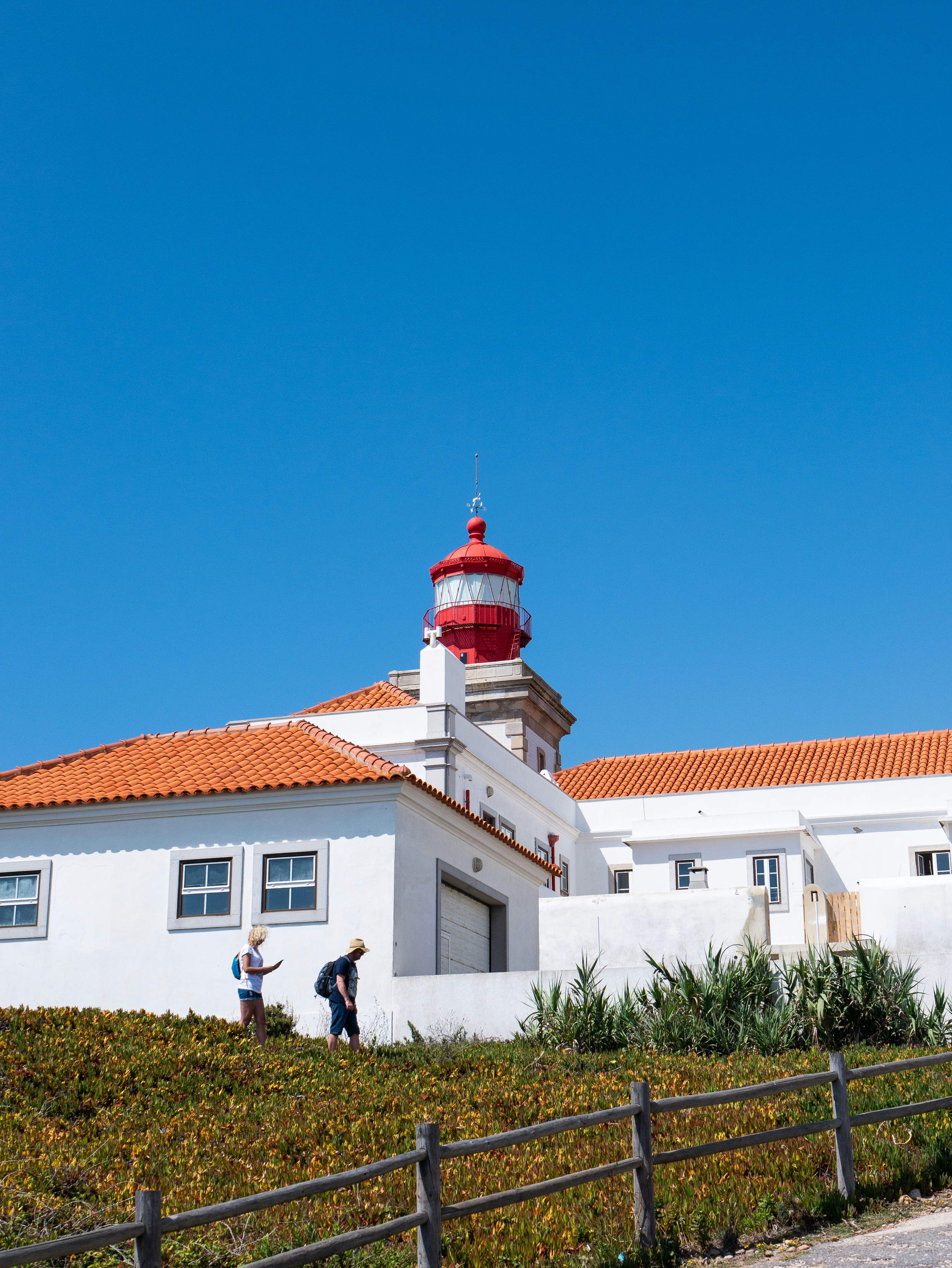 Historic lighthouse stands prominently against a clear blue sky, with visitors exploring the surrounding landscape.
