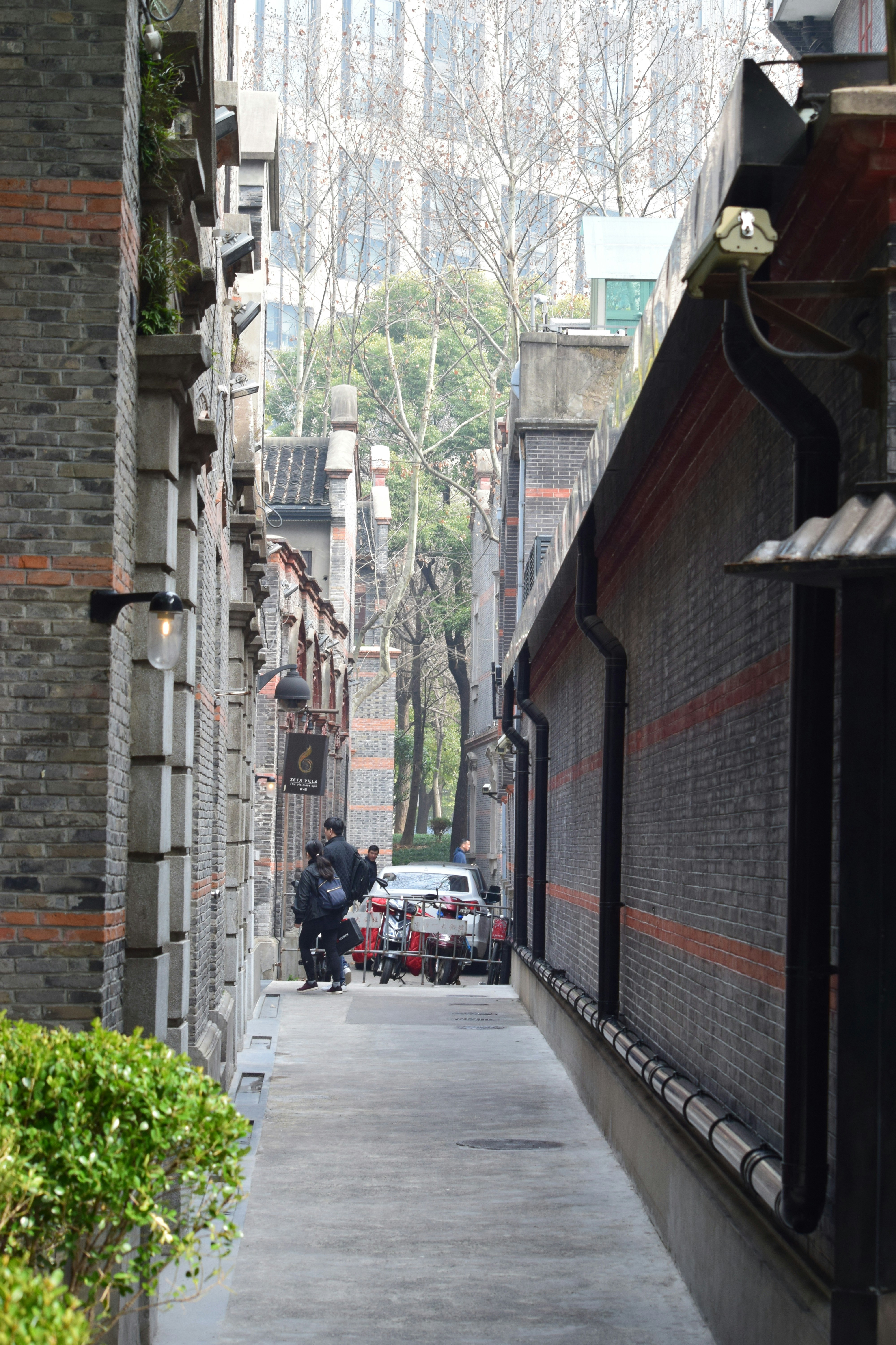 A narrow alleyway flanked by brick buildings, showcasing individuals engaged in daily activities amidst a blend of modern and historical architecture.