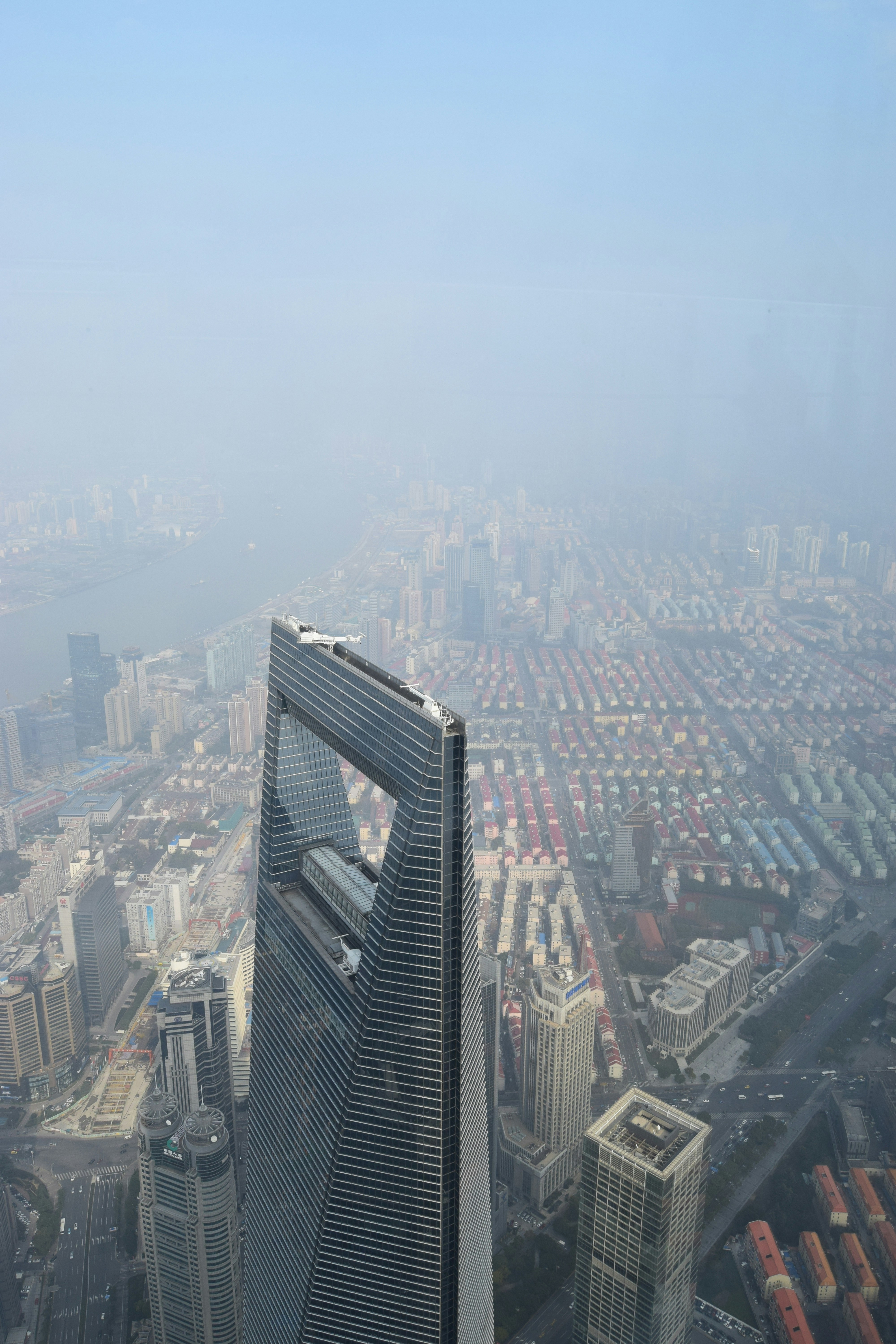 View from above the Shanghai skyline, highlighting the distinctive shape of the Shanghai Tower amidst a sprawling cityscape shrouded in haze.