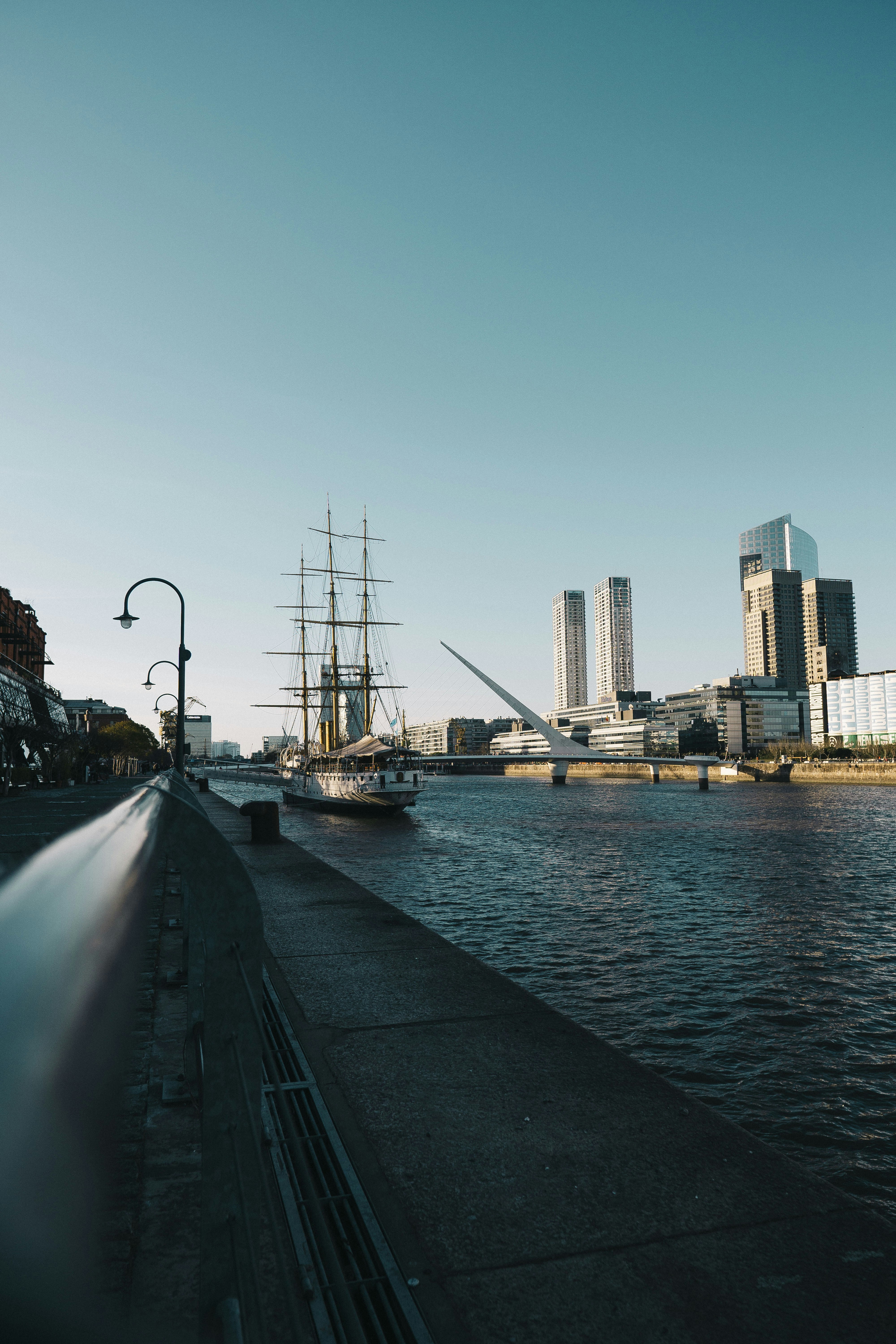 A historic tall ship navigates the waters beside modern skyscrapers, showcasing the blend of tradition and contemporary architecture. The scene captures the essence of urban life along the waterfront.
