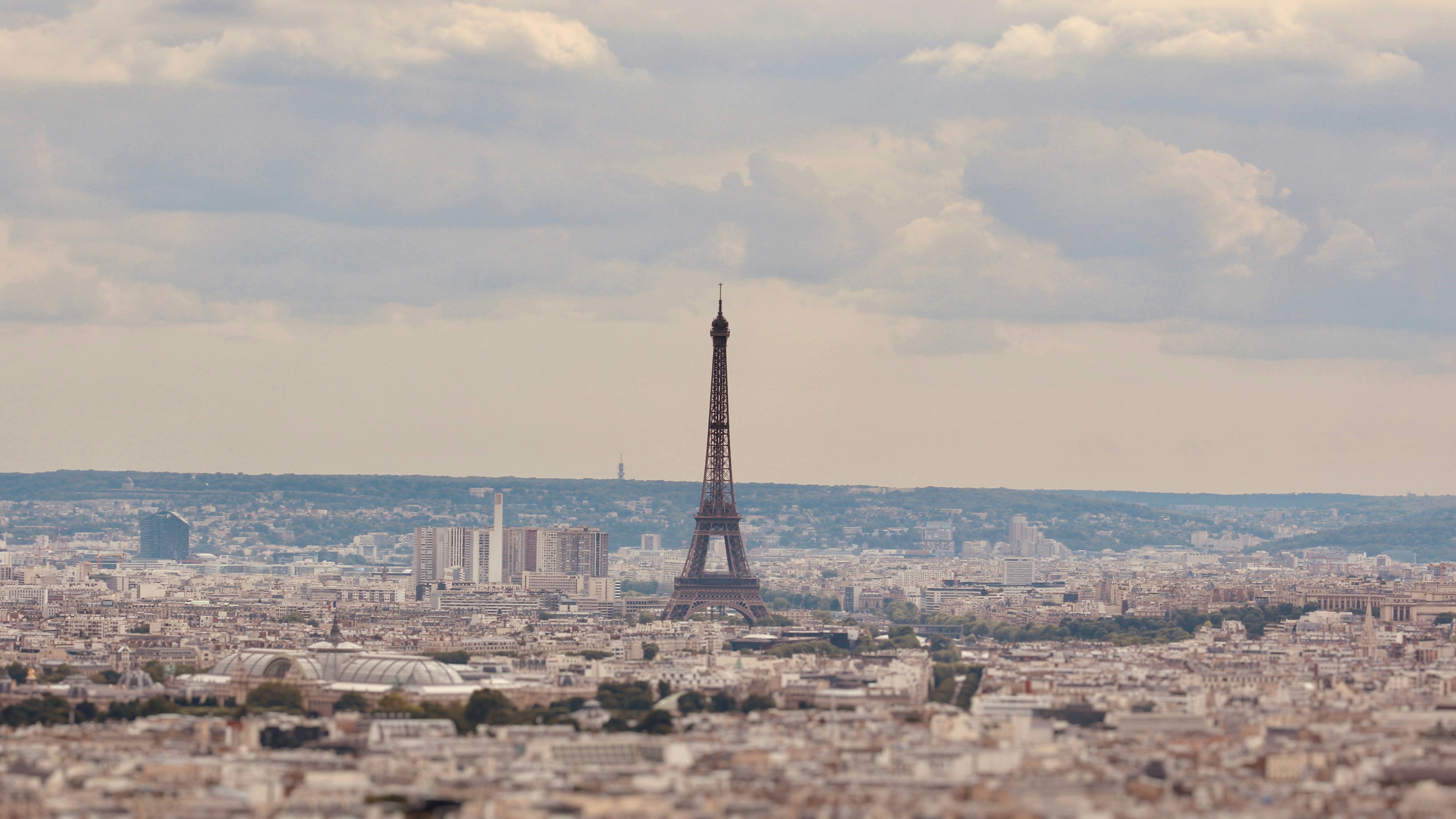 Eiffel Tower rising prominently above the sprawling cityscape of Paris under a cloudy sky.