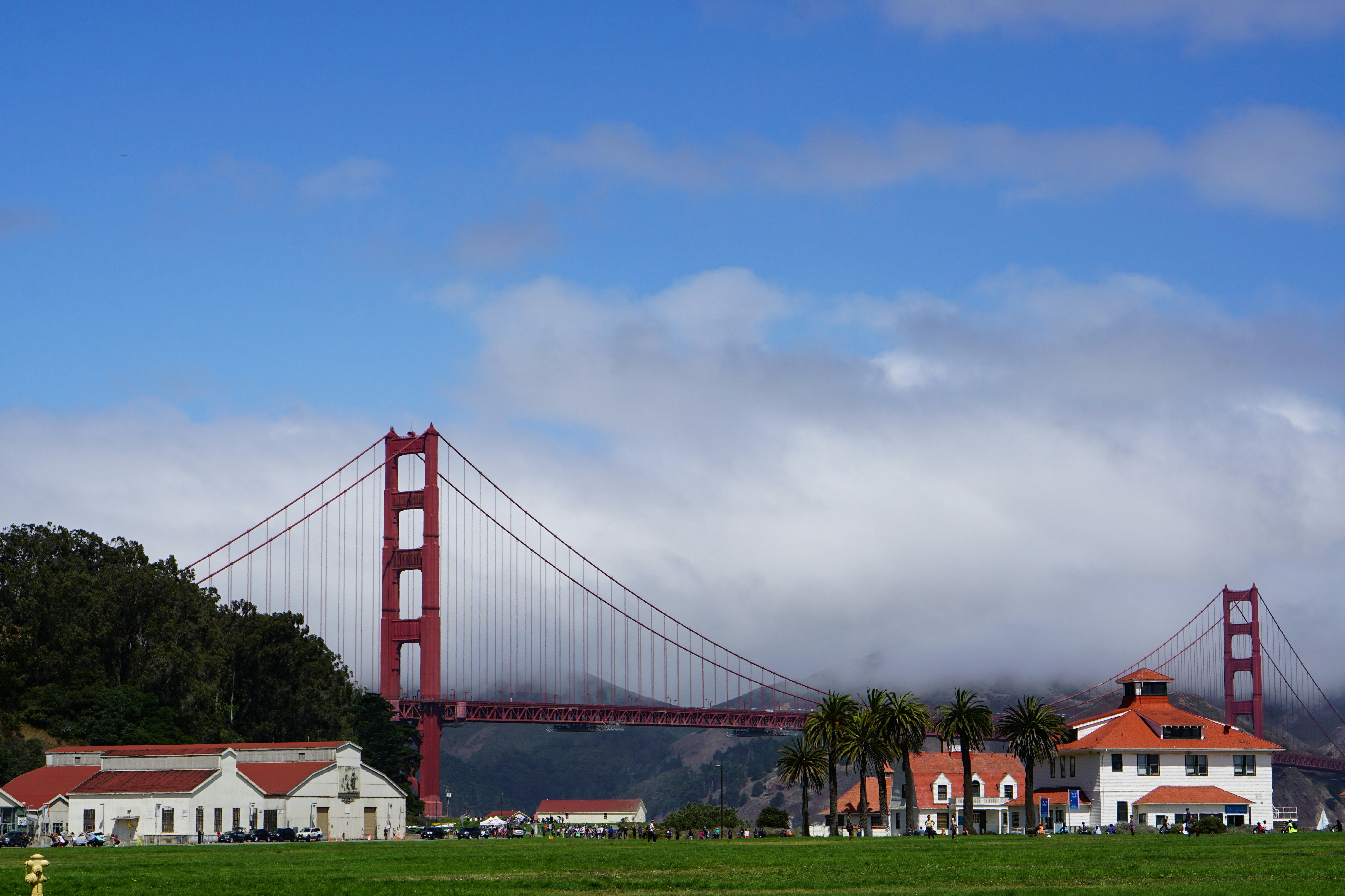 Golden Gate Bridge rises majestically above the lush landscape, framed by clouds and historic buildings below.