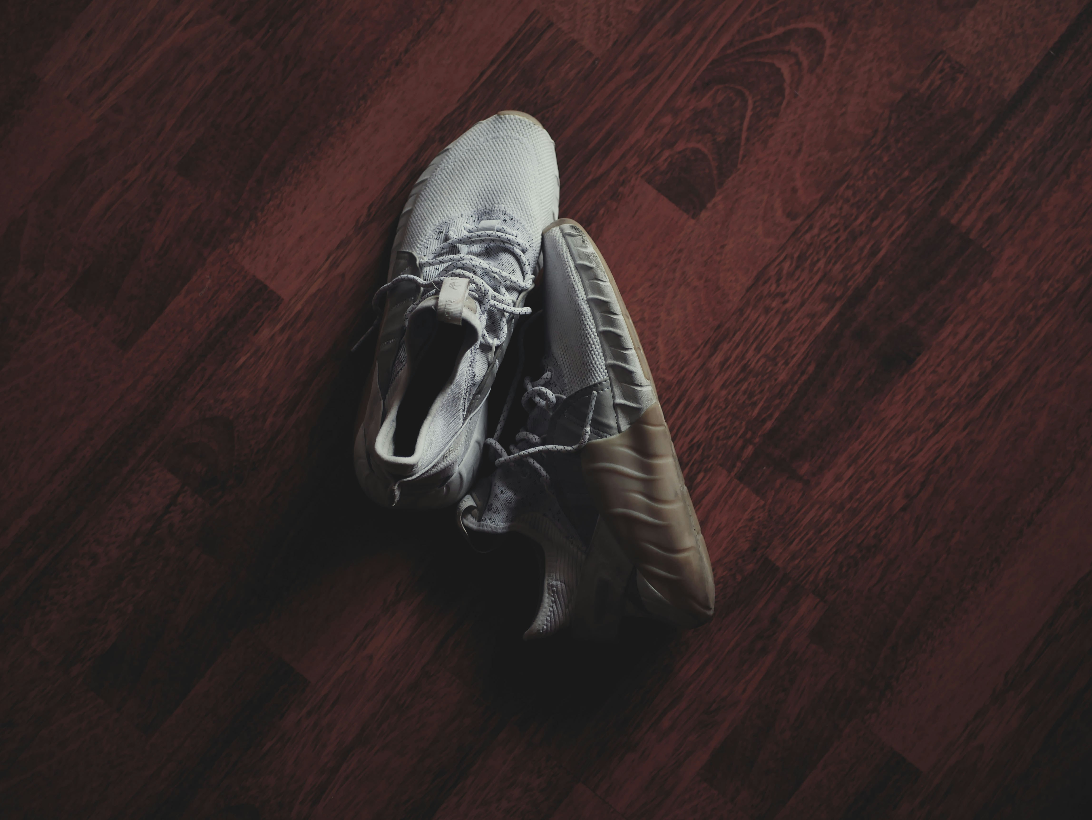 Pair of gray sneakers resting on a rich wooden floor under soft lighting.