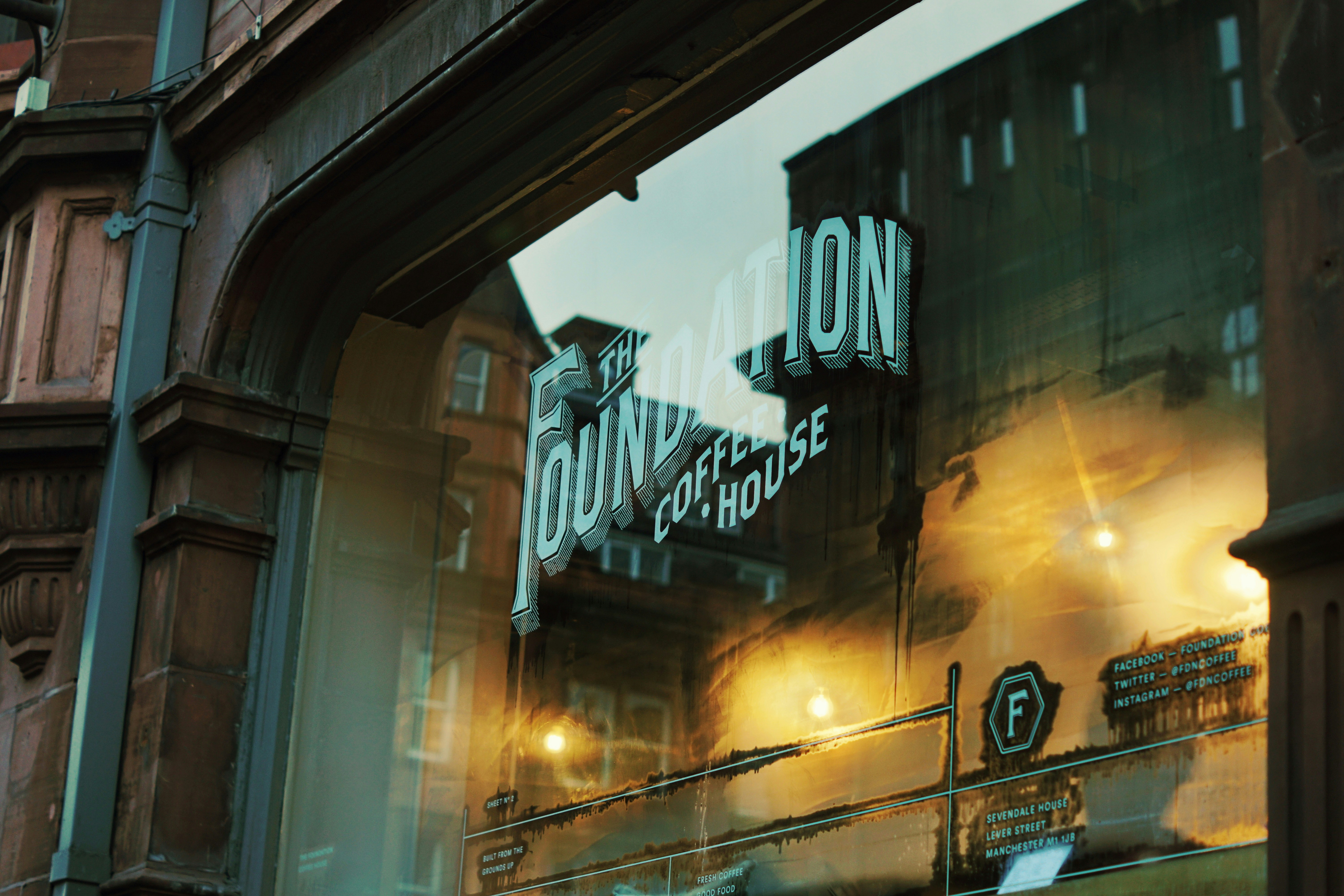 Warm glow of cafe lights reflected in a large window with a city street backdrop.