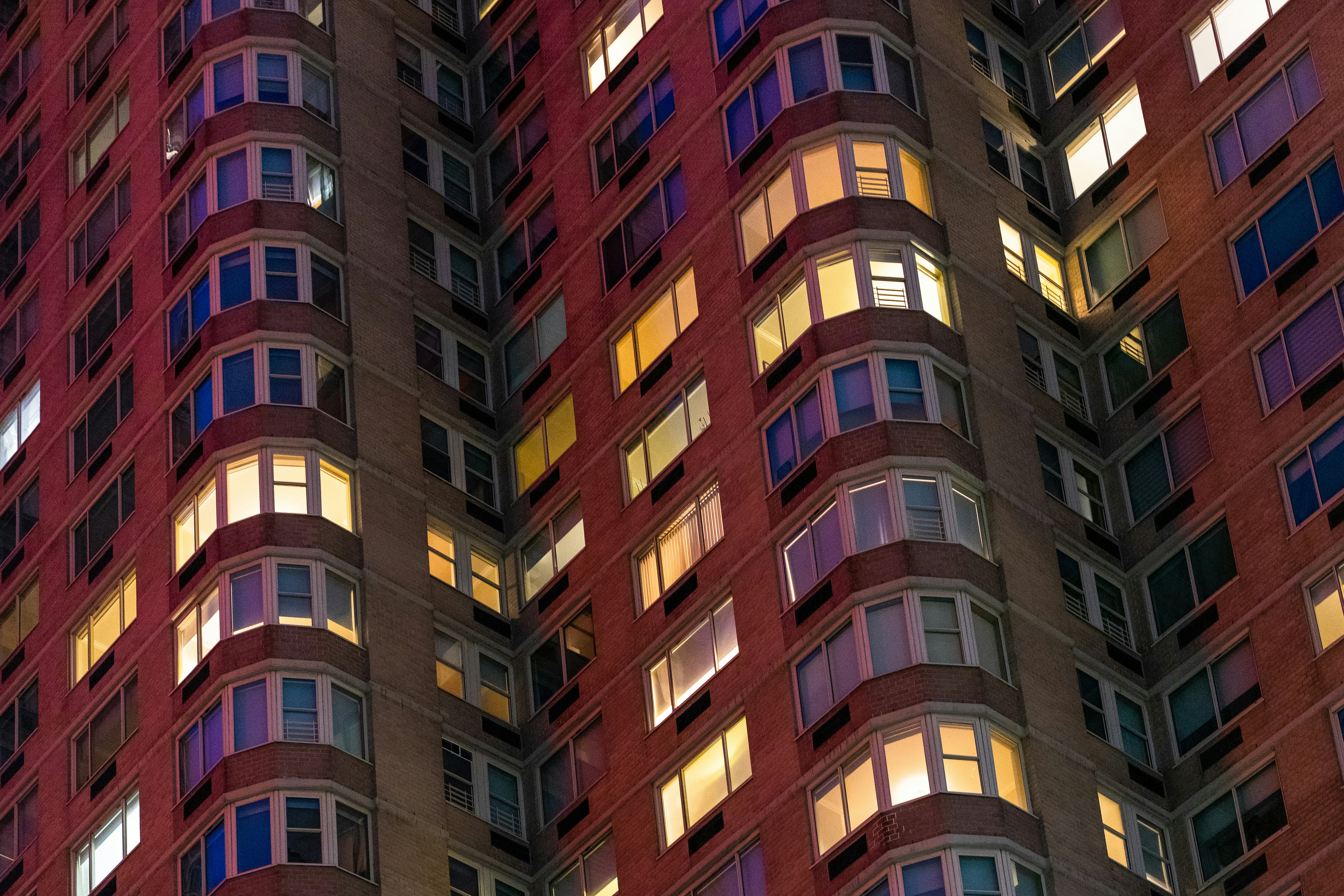 Illuminated apartment windows create a mosaic of light against a darkened building facade at night.