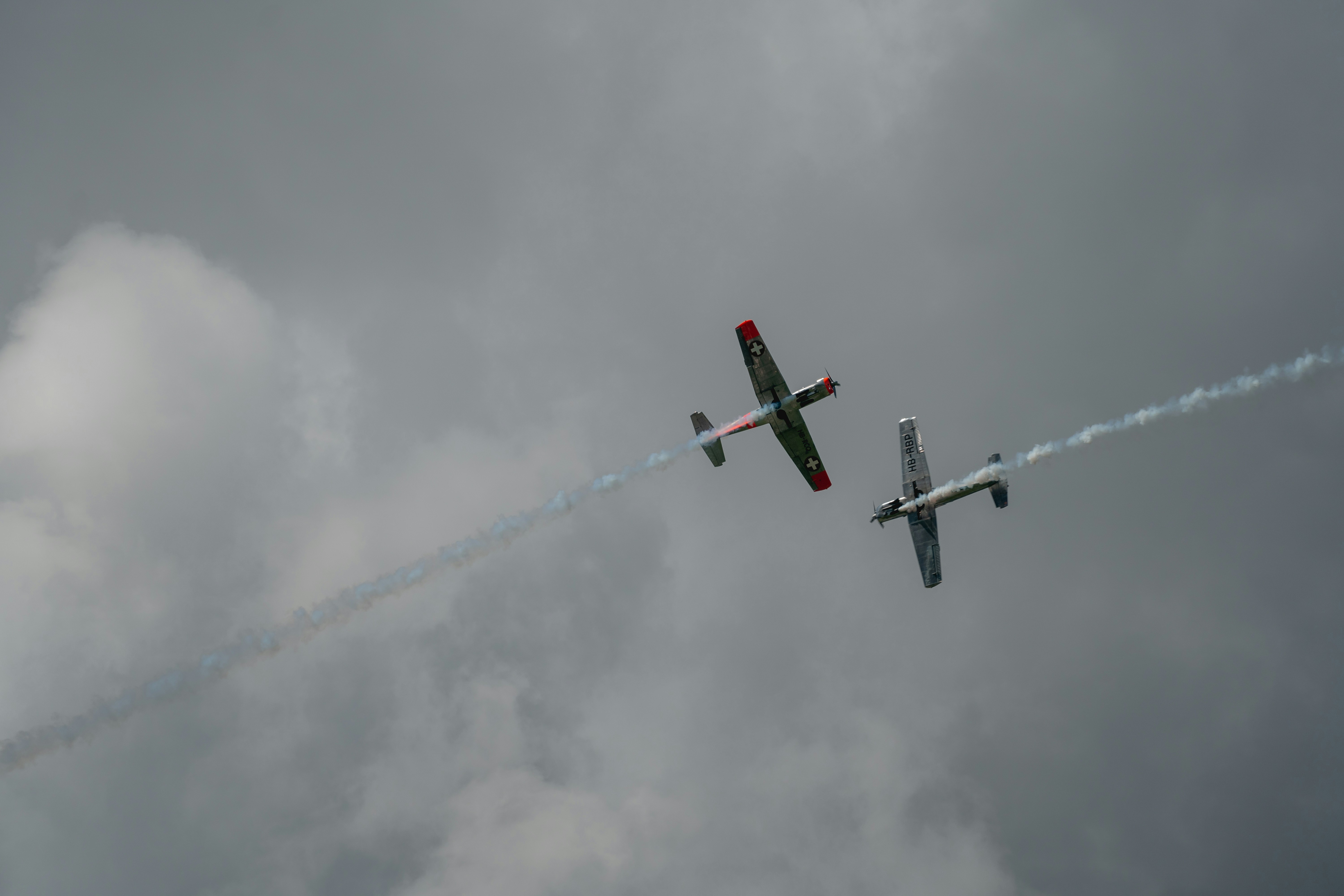 Twin aerobatic planes cross paths, weaving smoke trails through a cloudy sky