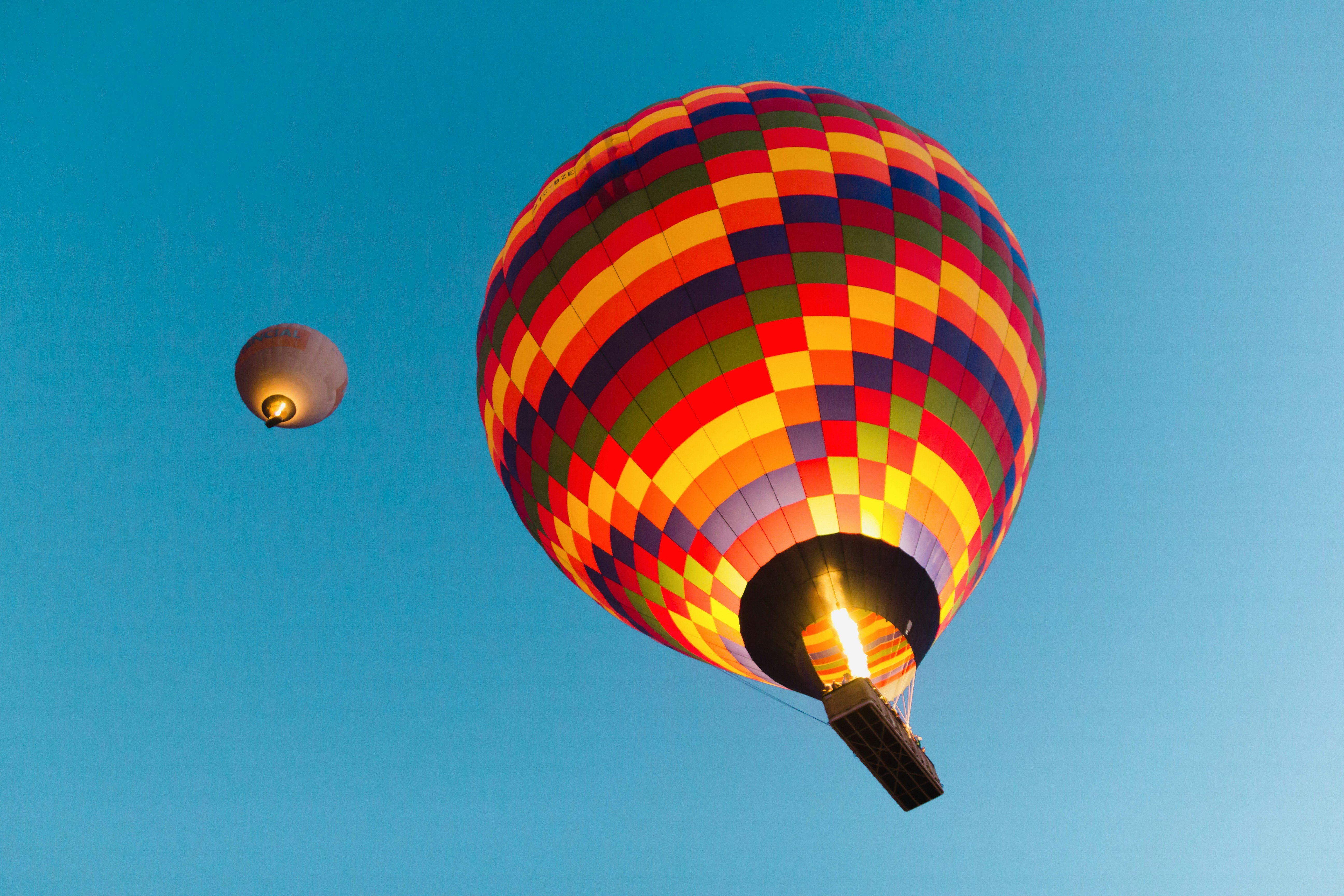 Quilted Flame in the Sky: A bold color-block hot air balloon rises with a distant companion against a pristine blue backdrop