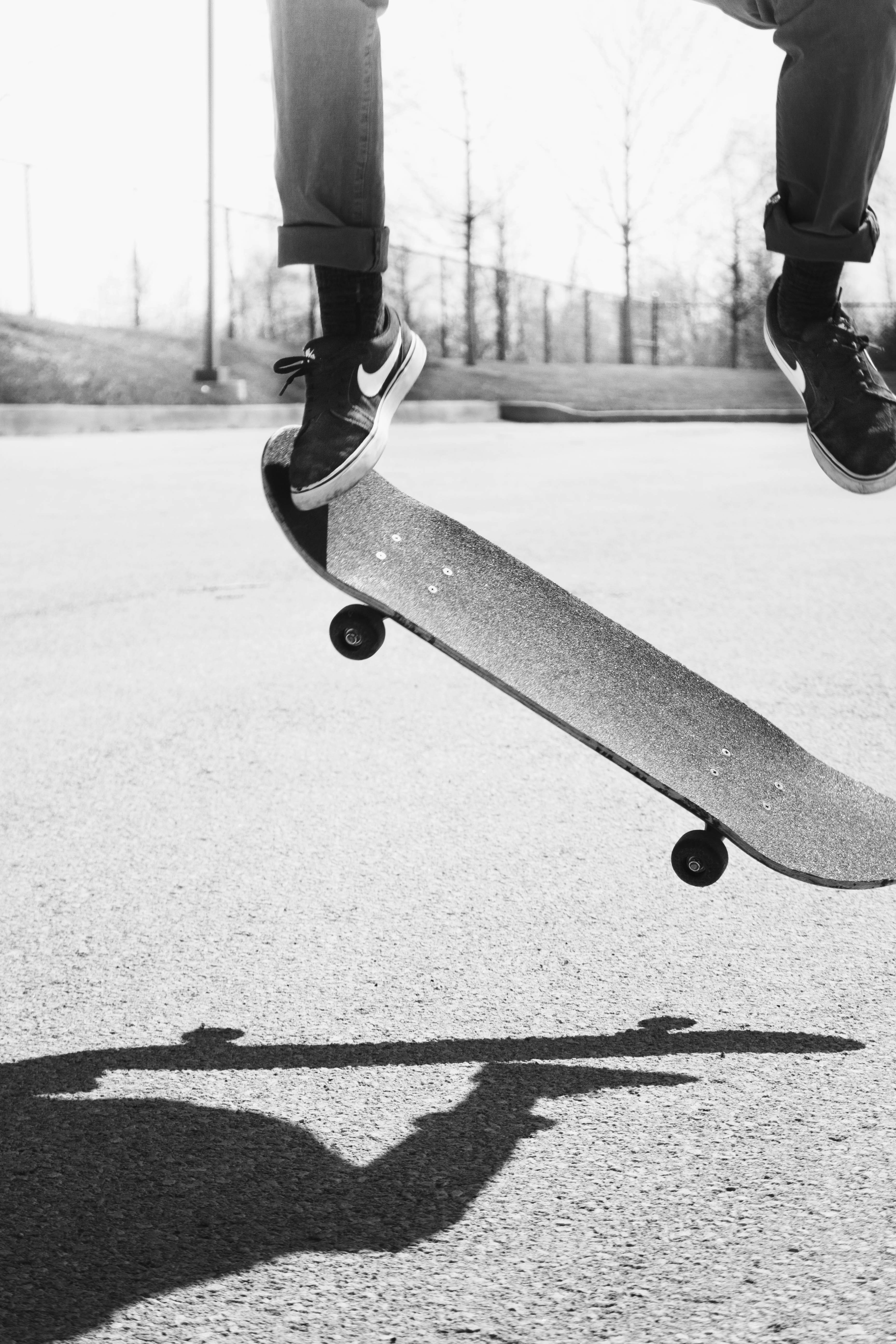 Skateboarder performing a trick with a skateboard elevated above the ground, casting a shadow on the pavement.