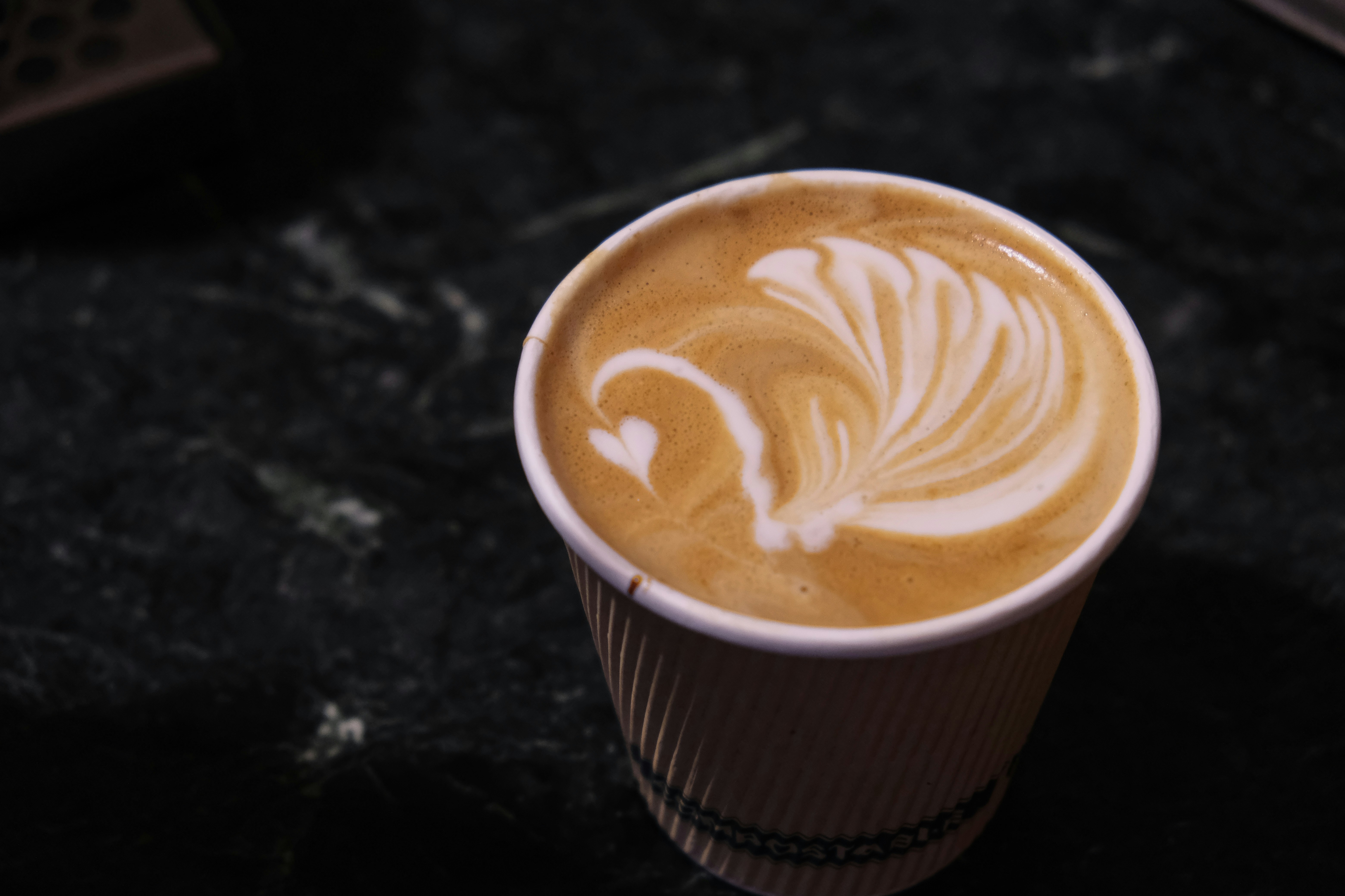 Intricate latte art resembling a swan with a heart, crafted atop a cup of coffee. The rich, creamy texture contrasts with the dark surface beneath.
