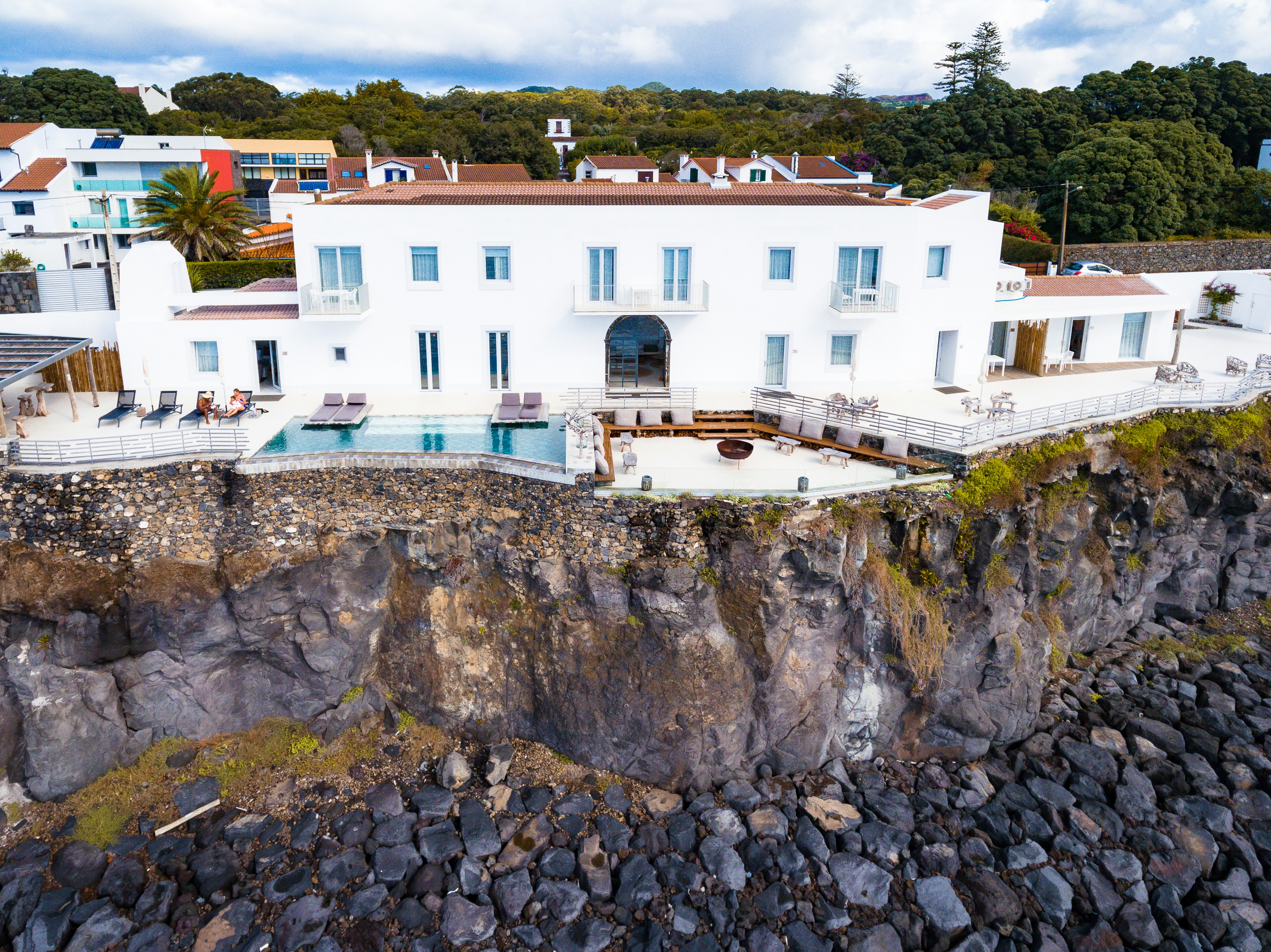 White villa perched on a rocky cliffside overlooking a rugged coastline under a partly cloudy sky.