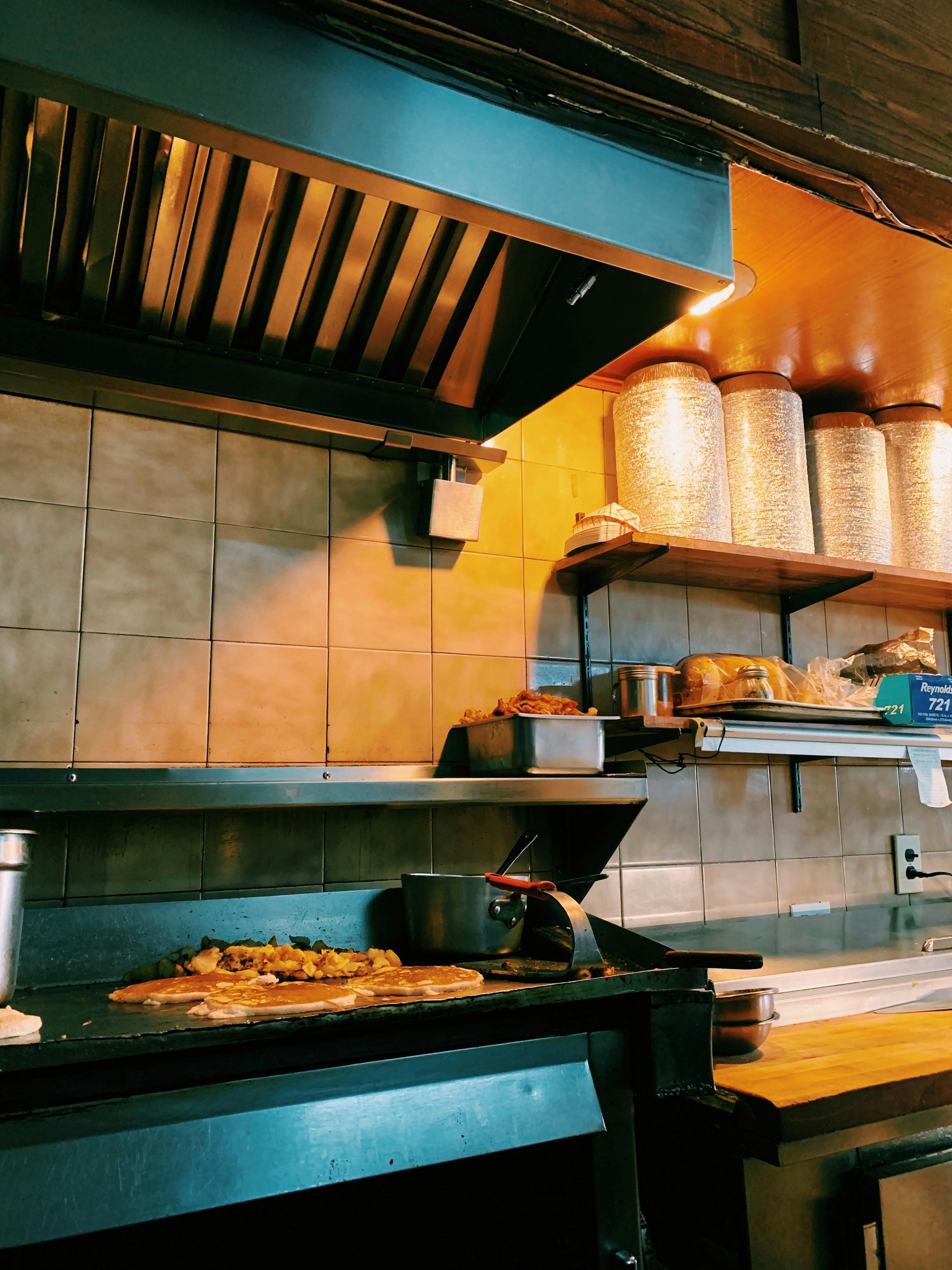 Griddle Glow: Food Sizzles Under Kitchen Hood