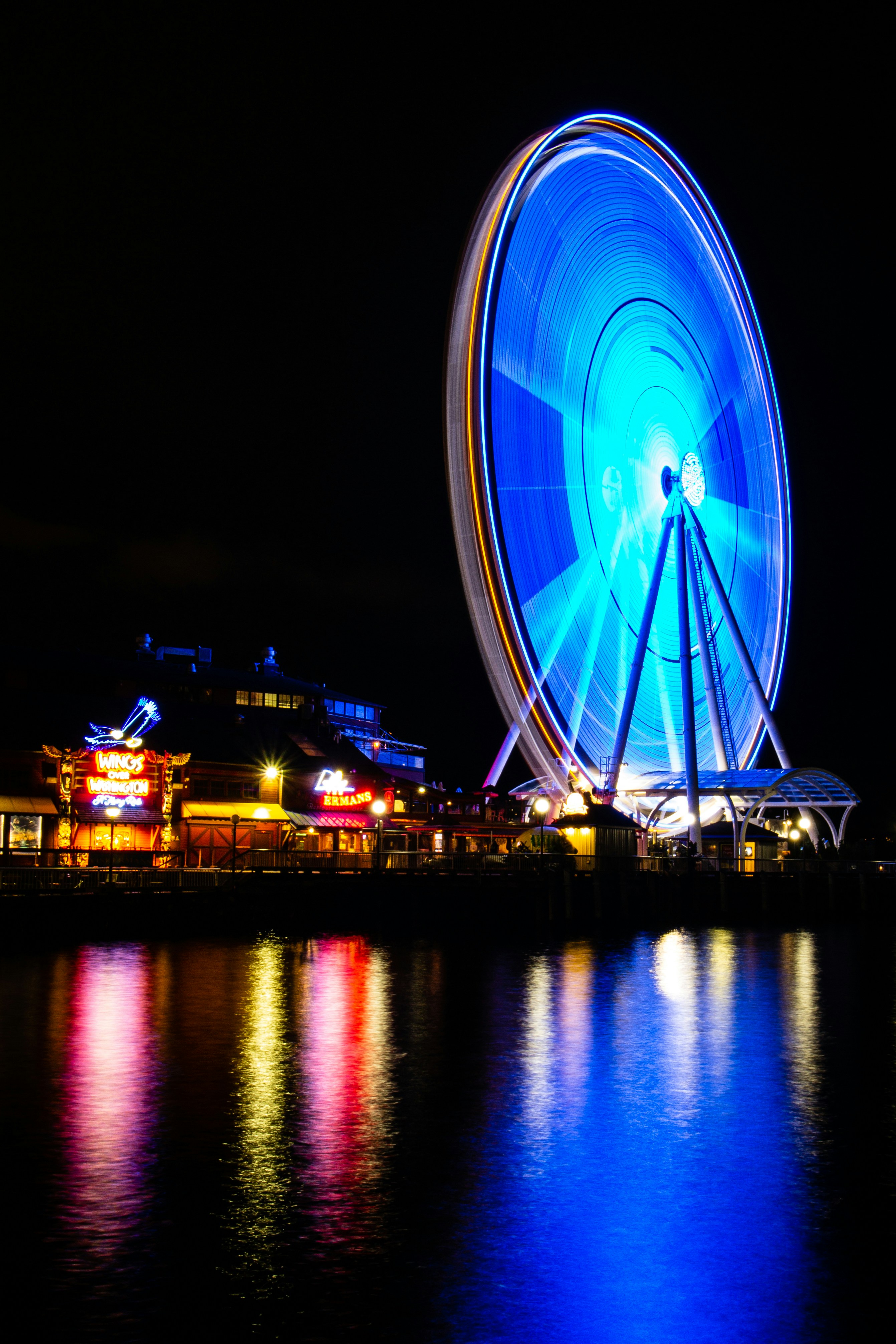 Spinning Ferris wheel glowing in vivid blue over a waterfront, with vibrant reflections on the water below.