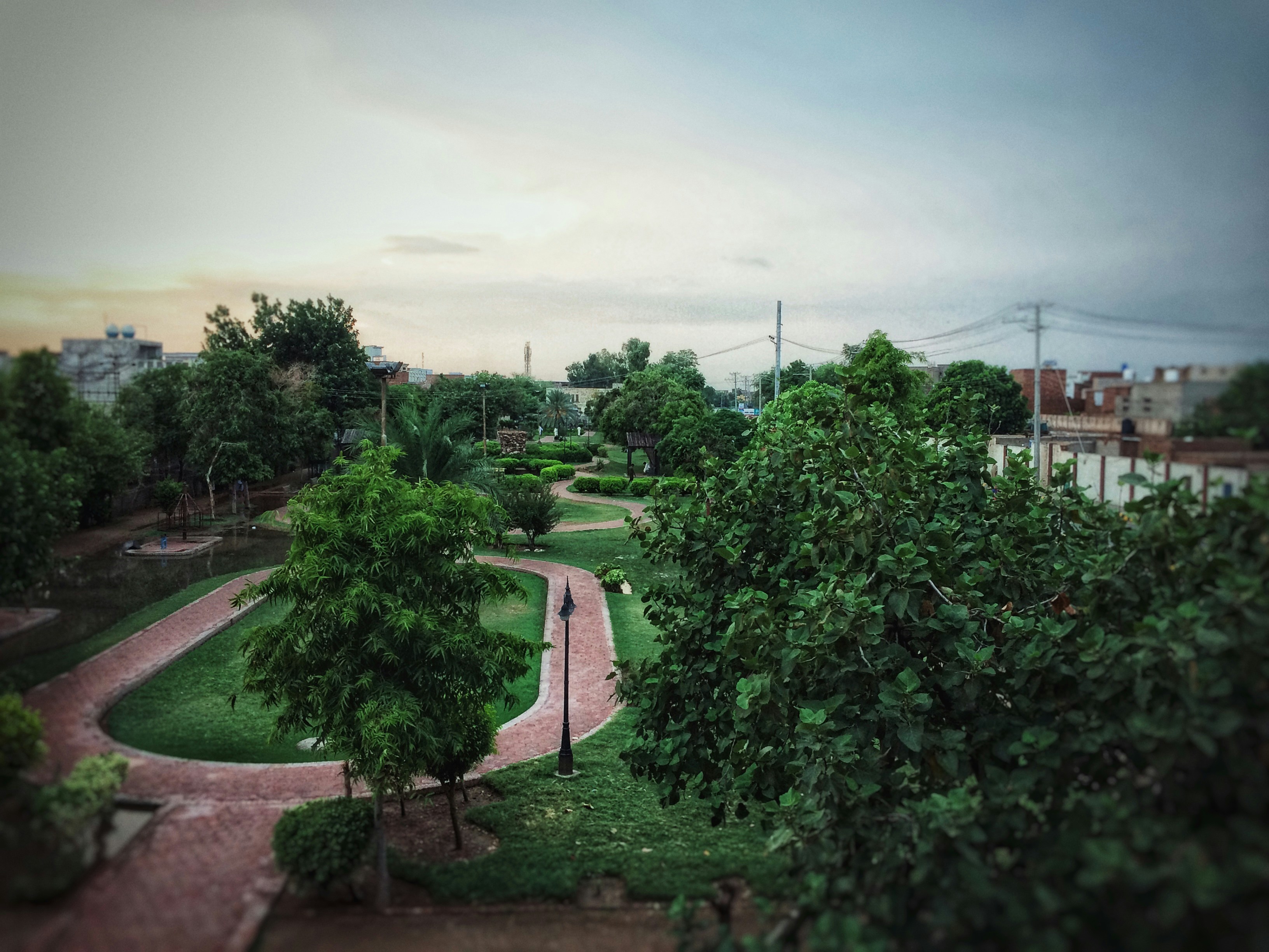 Winding brick paths meander through a lush green park as evening approaches.