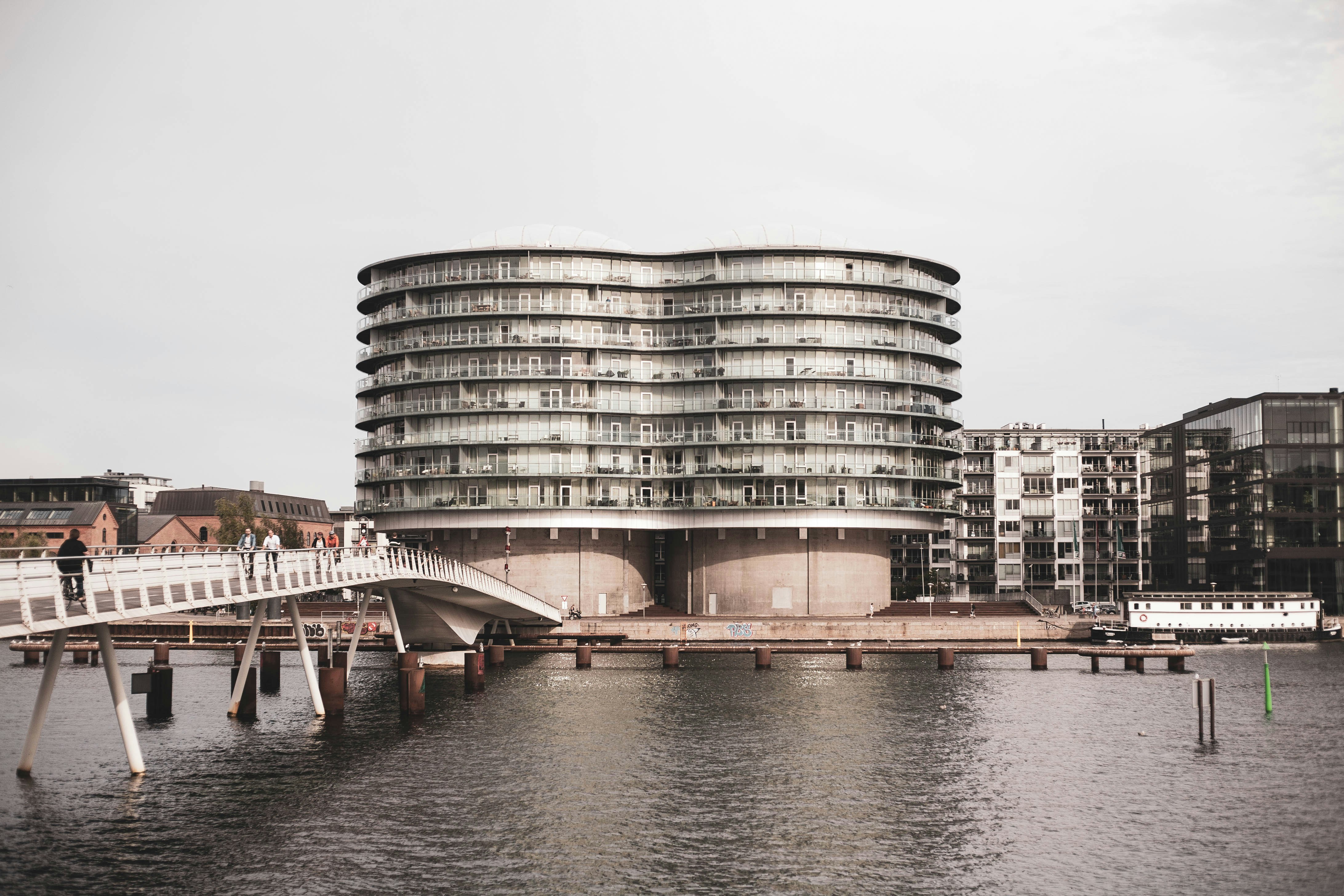 A sleek, modern building with curved glass facades stands beside a serene waterway, showcasing contemporary urban design.