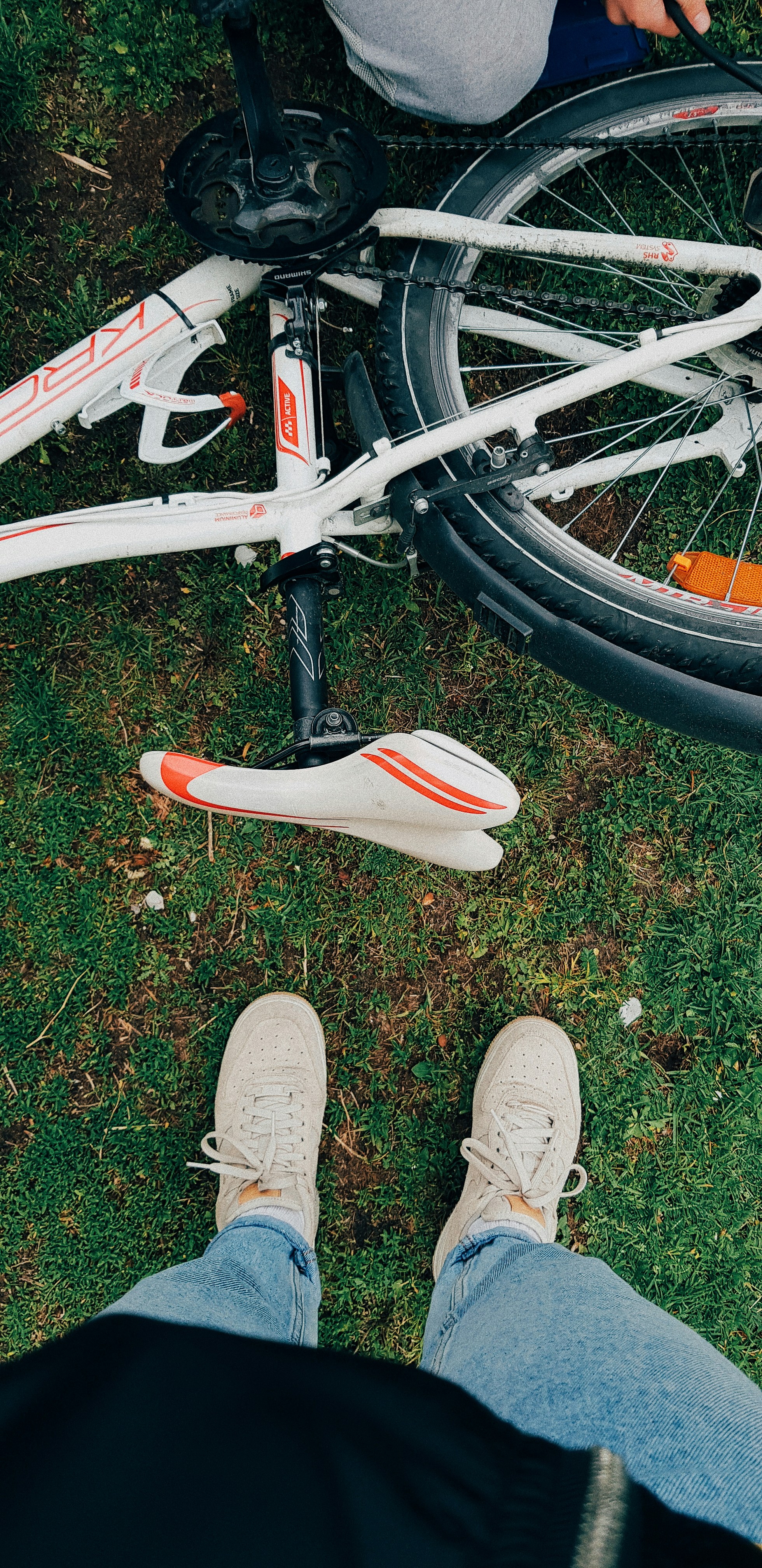 Overhead Pause: White Bicycle Resting on Grass with Grounded Sneakers