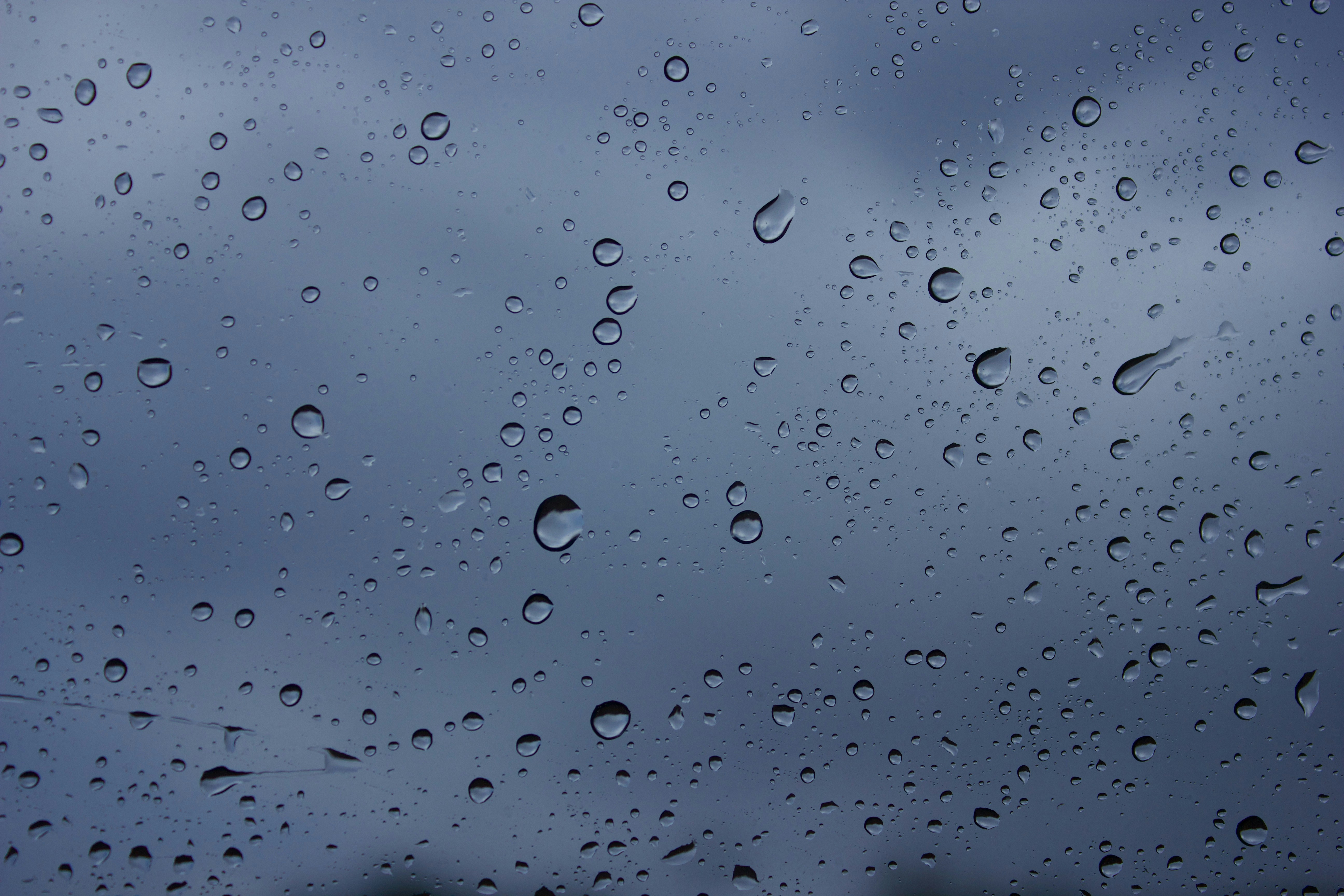 Raindrops on a window against a backdrop of dark, cloudy sky.
