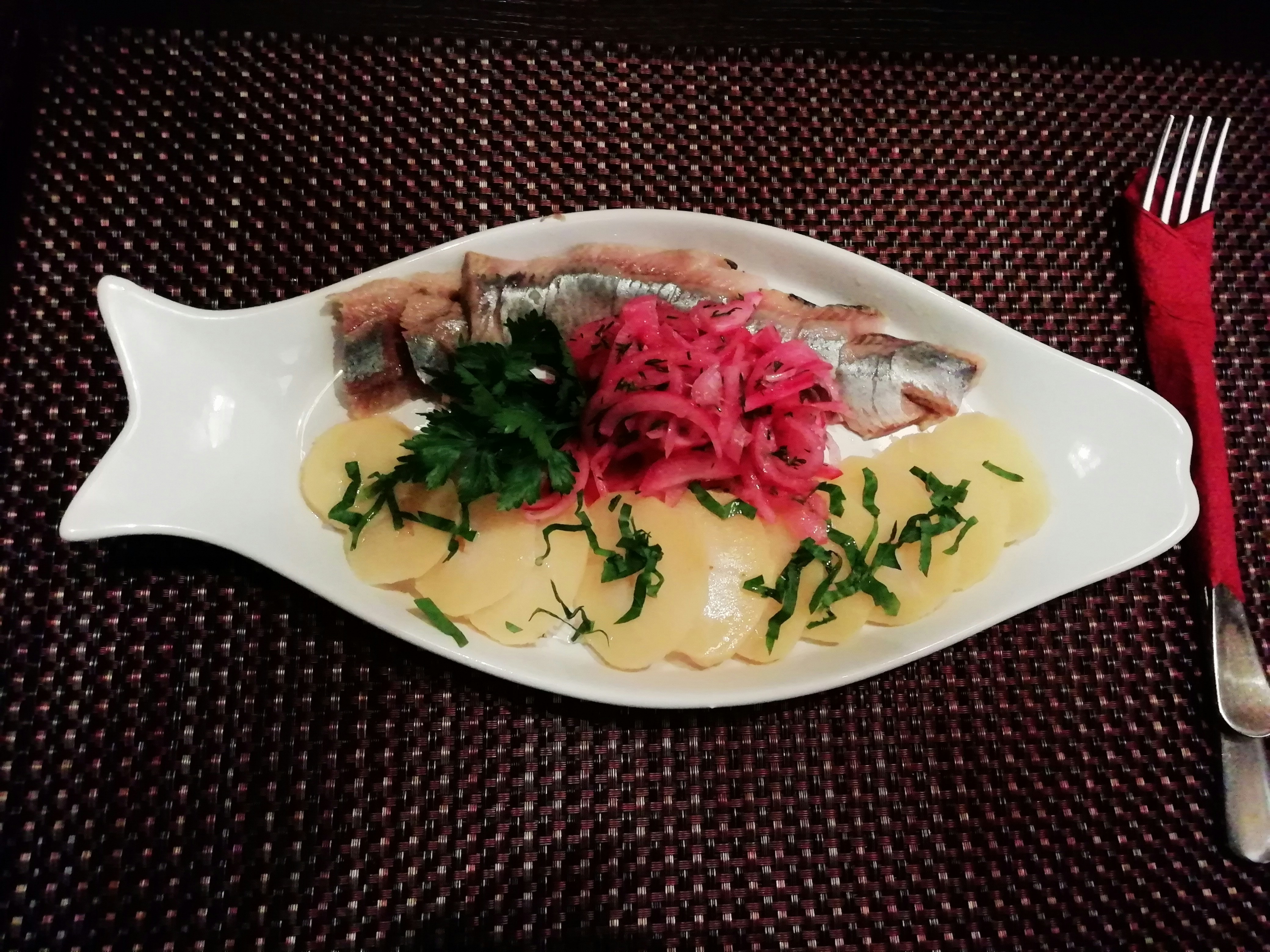 Delicately plated fish with vibrant pickled onions and fresh herbs on a uniquely shaped dish, showcasing a creative culinary presentation.