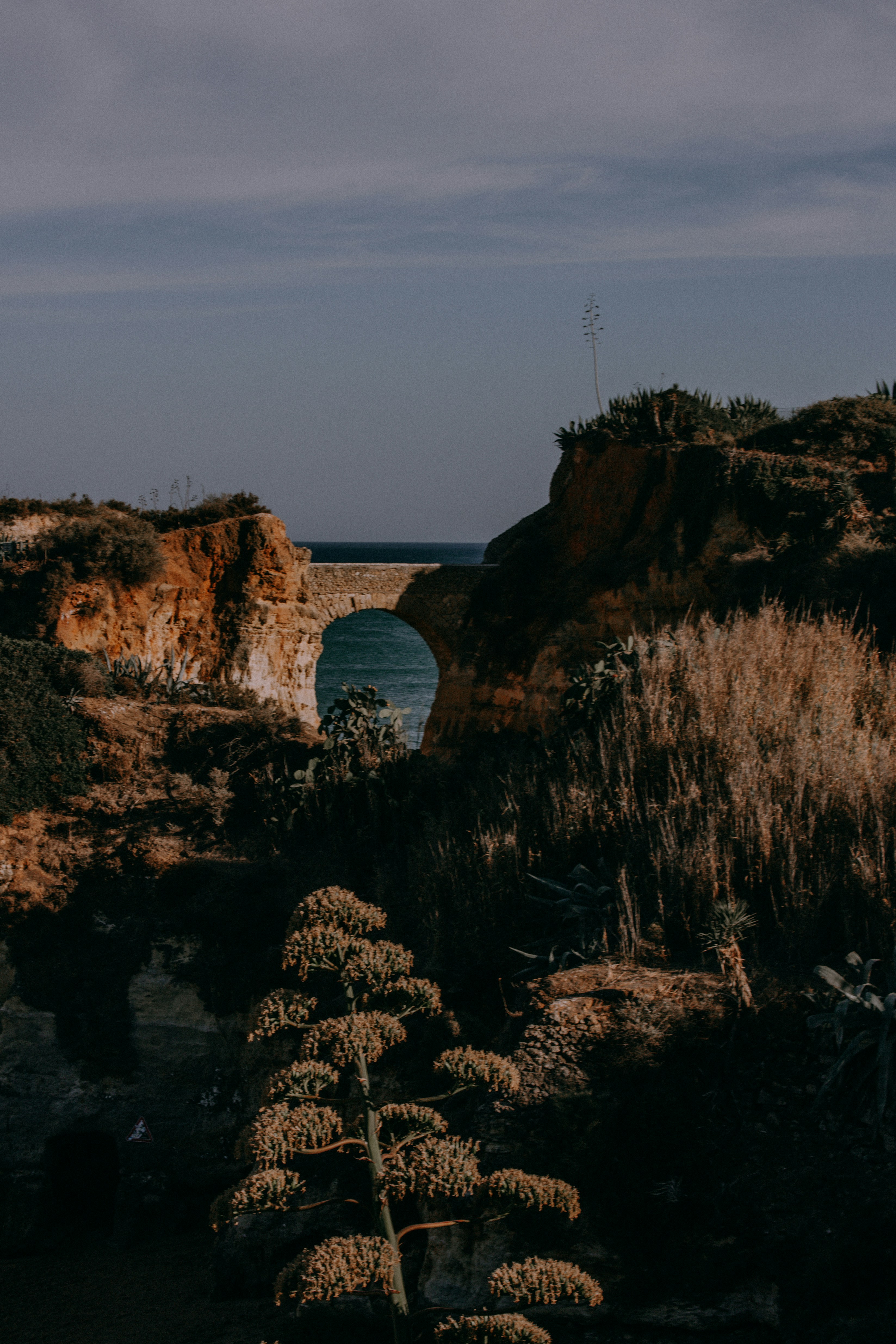 Natural stone archway bridging rocky cliffs with the ocean visible beyond, surrounded by lush vegetation.