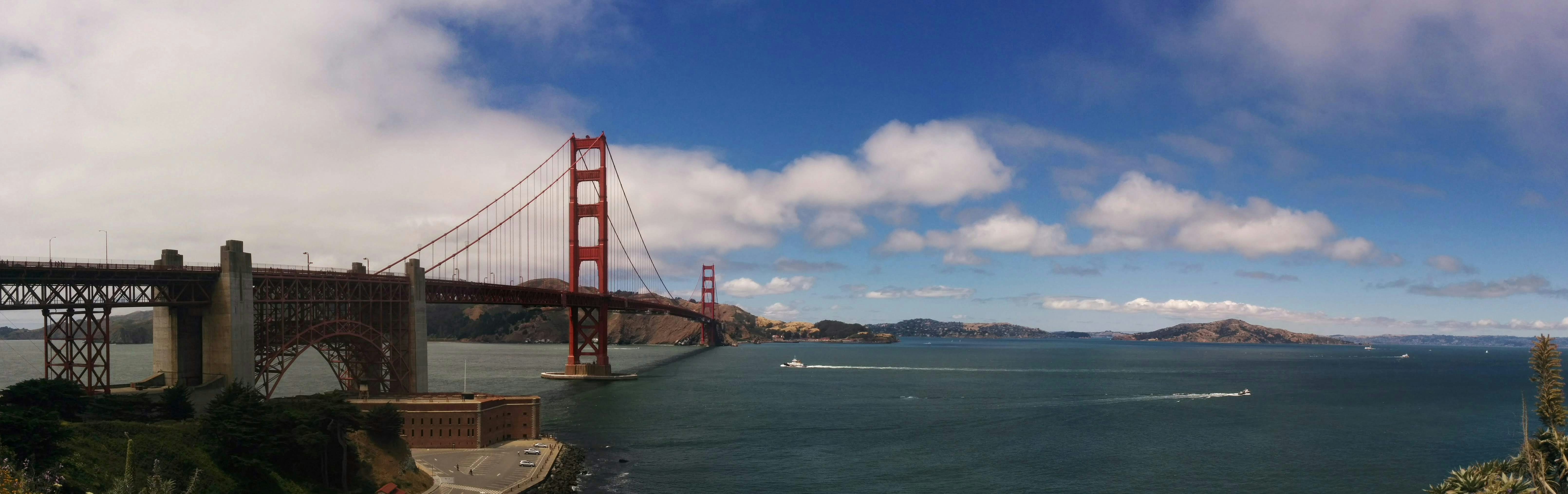 Panoramic view of the Golden Gate Bridge over calm blue bay, with distant hills and a clear sky.