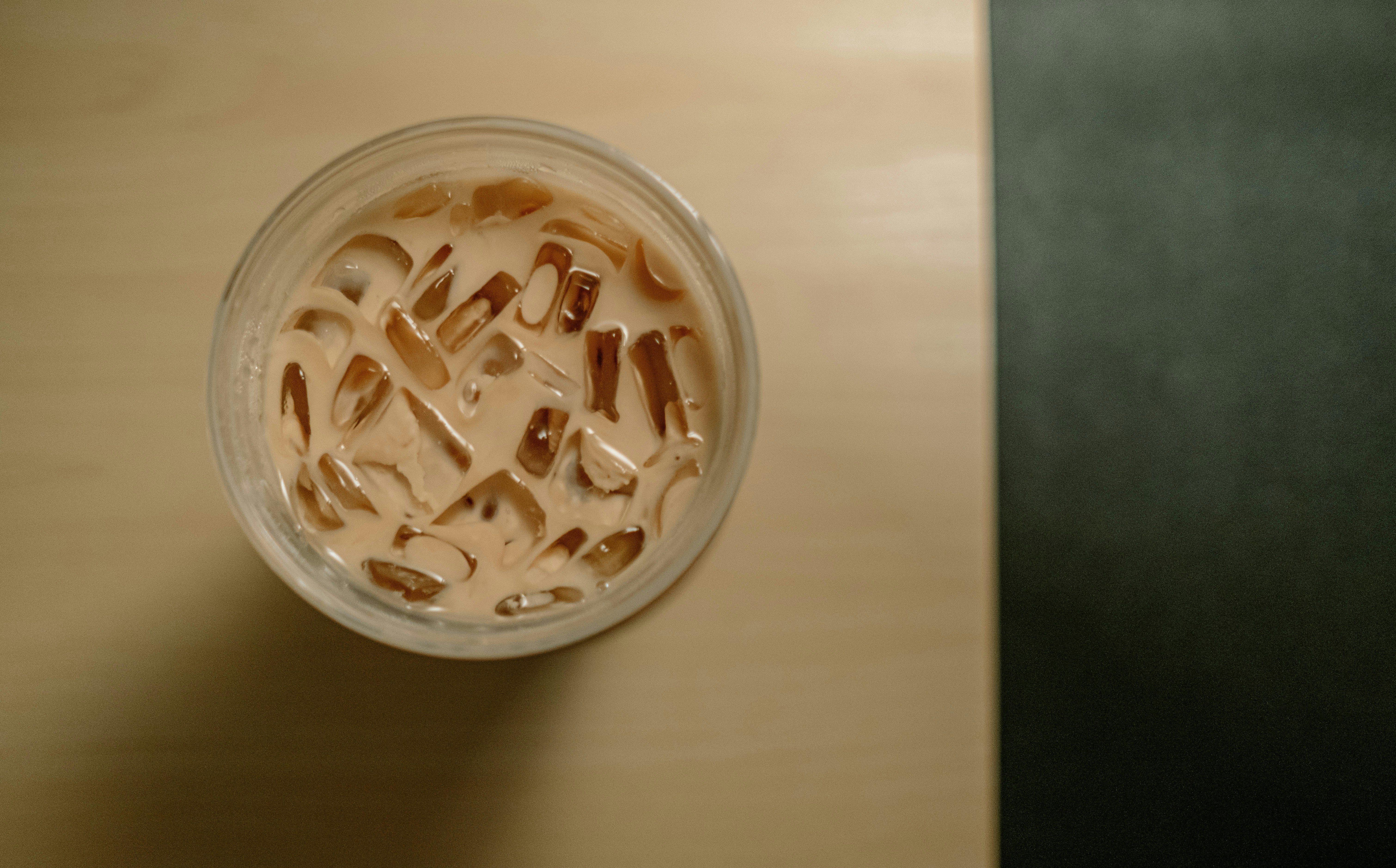 A top-down view of a cup filled with iced coffee, showcasing the creamy texture and ice cubes against a wooden surface.