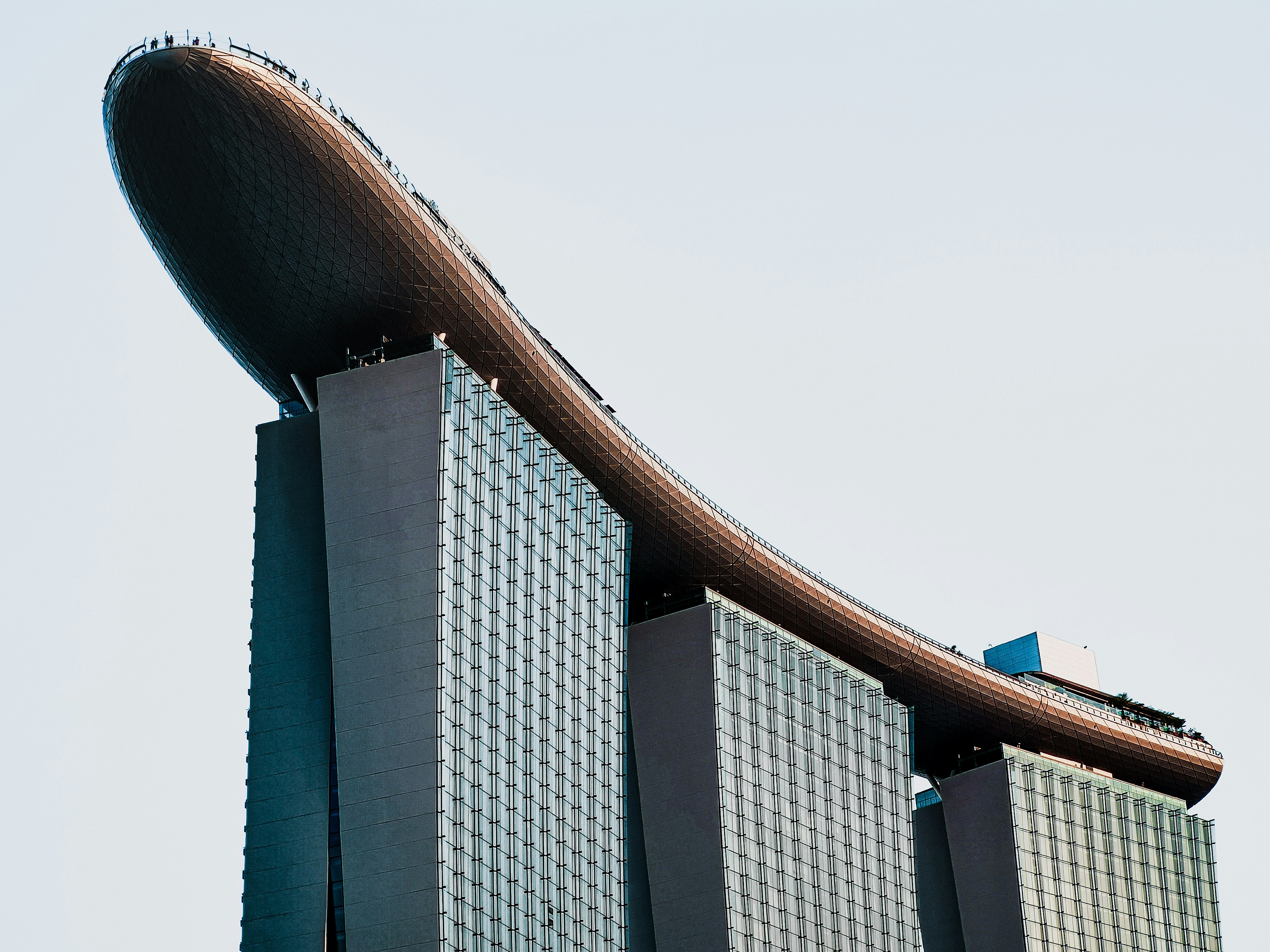 Architectural photograph capturing glass towers topped by a curved, boat-like roof against a clear sky. The domed roof forms a bold focal point across the composition.