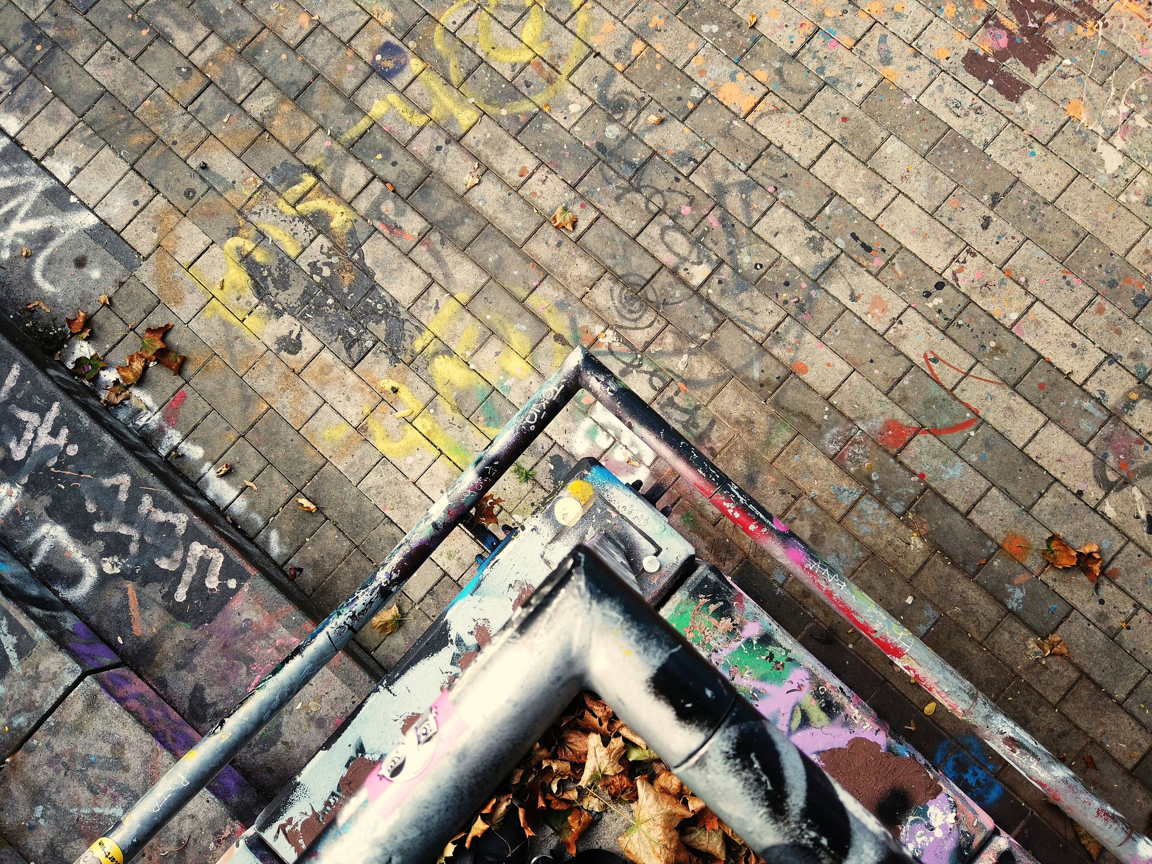 Colorful graffiti and fallen leaves on a textured brick pavement, showcasing urban artistry and seasonal change.