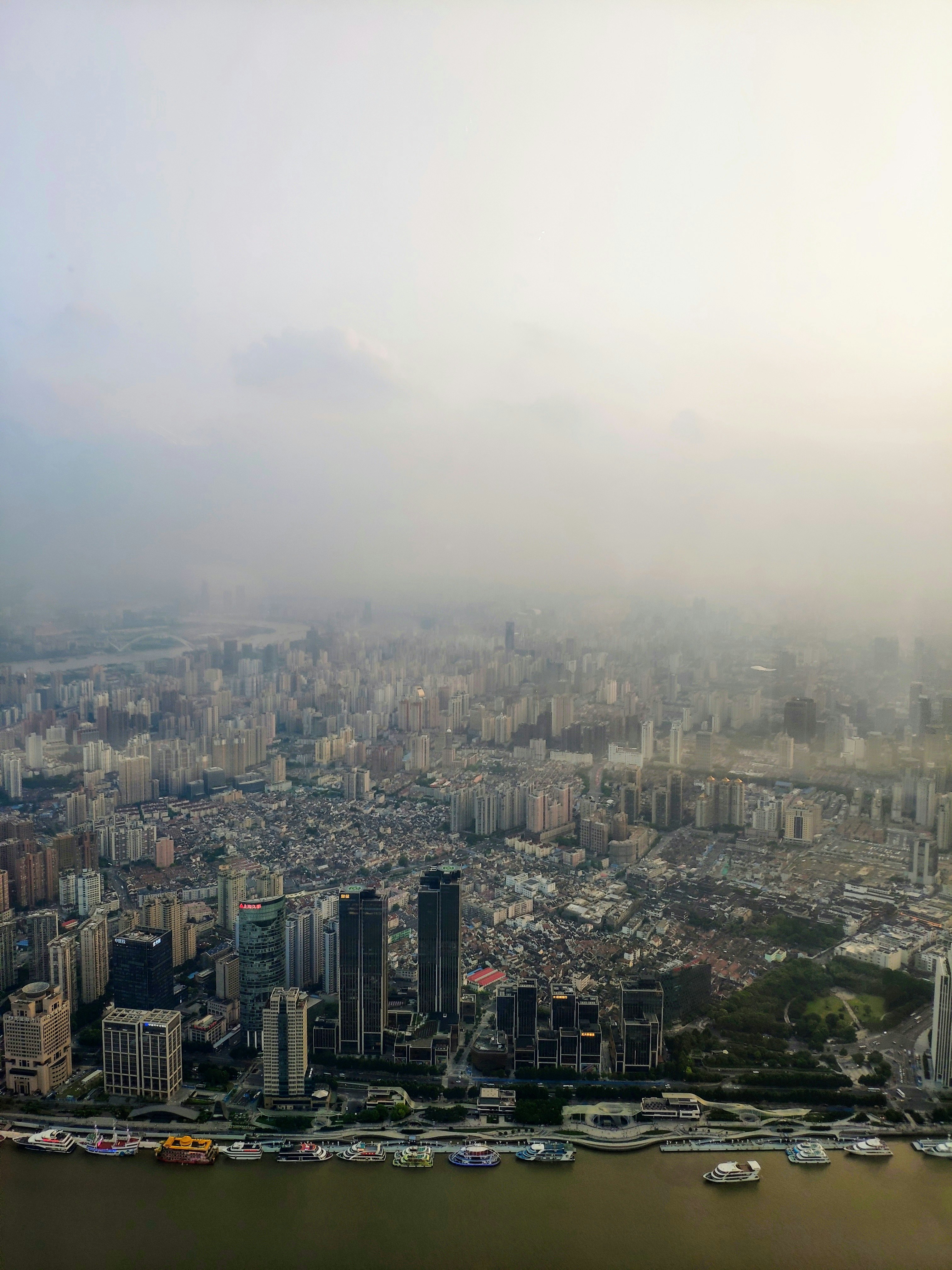 Aerial view of a sprawling urban landscape shrouded in mist, highlighting the contrast between modern skyscrapers and traditional neighborhoods along the riverbank.