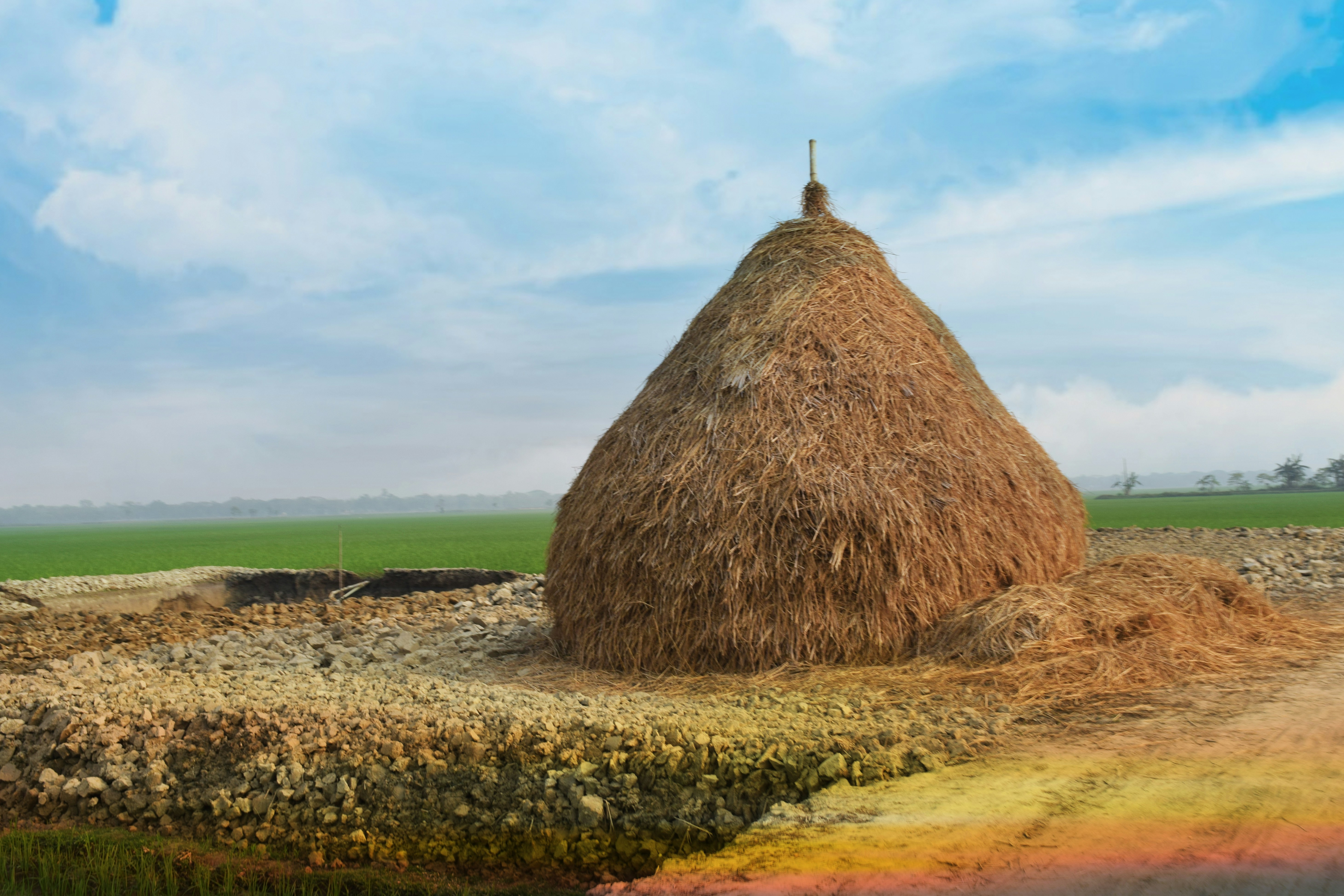A traditional haystack stands prominently in a lush green field under a bright blue sky, showcasing rural life and agricultural heritage.