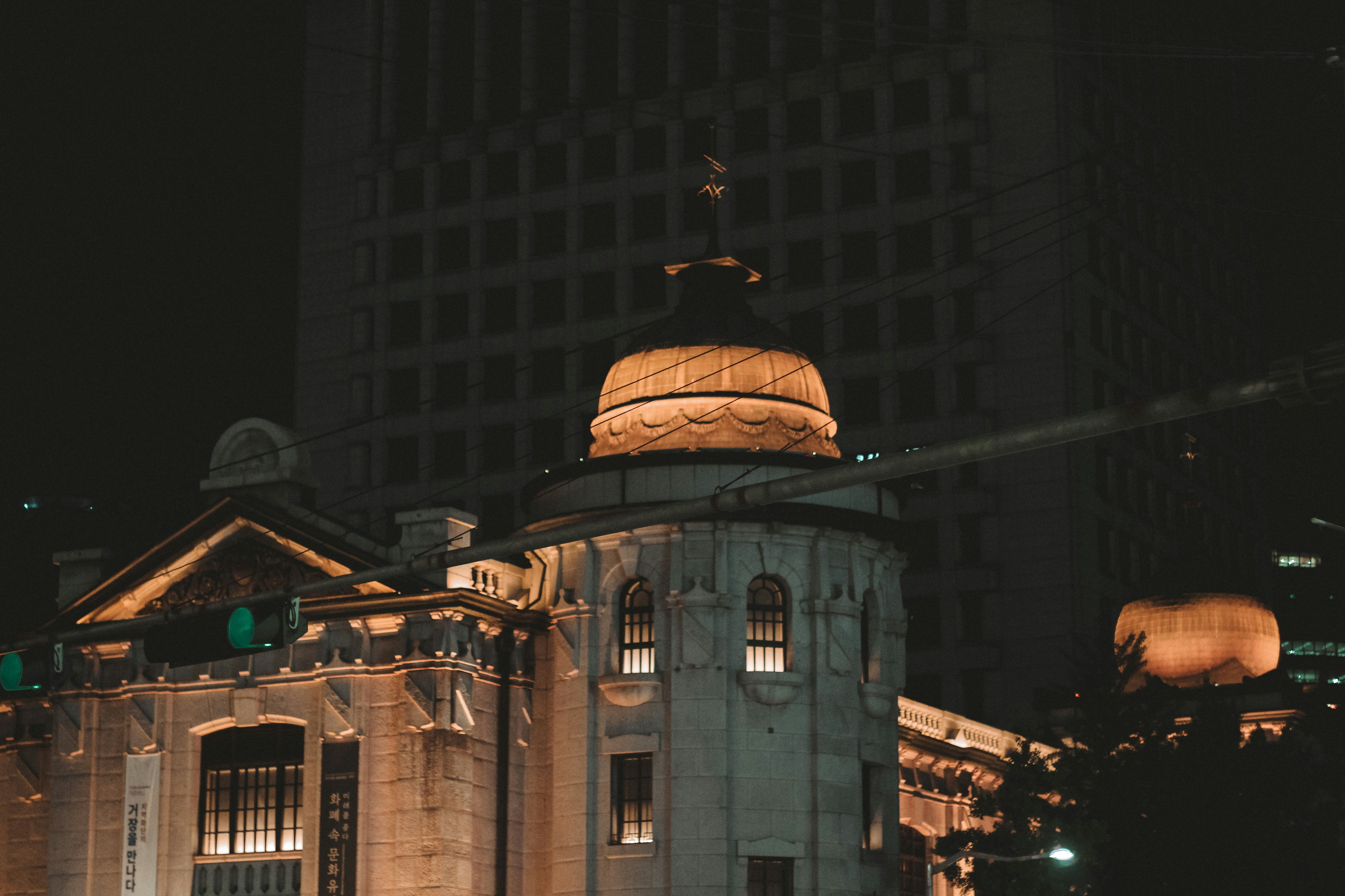 Historic building with a domed roof illuminated against a dark urban backdrop, showcasing intricate architectural details.