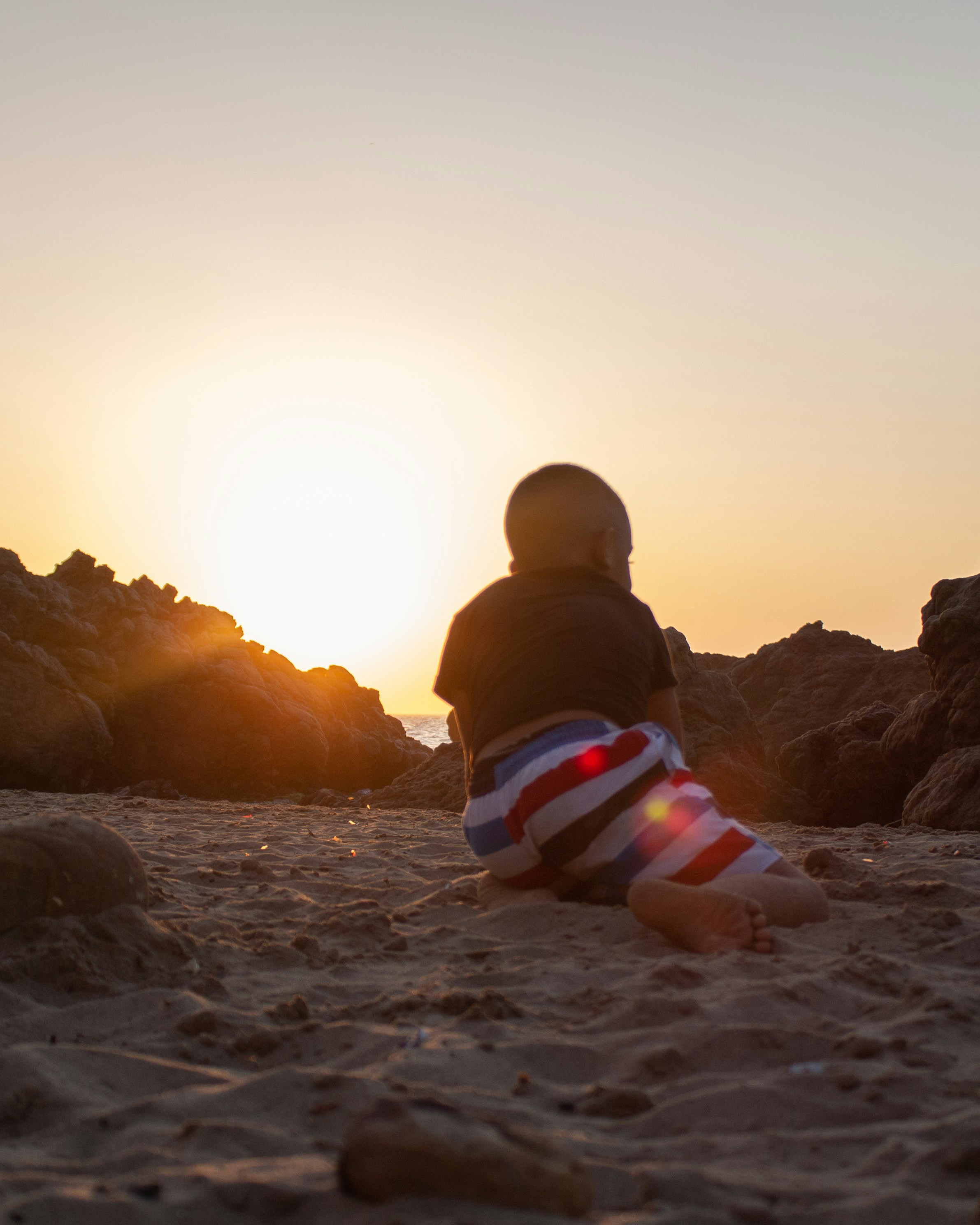 Sunlit Dusk on the Rocky Beach: A Baby Crawls Toward the Golden Light