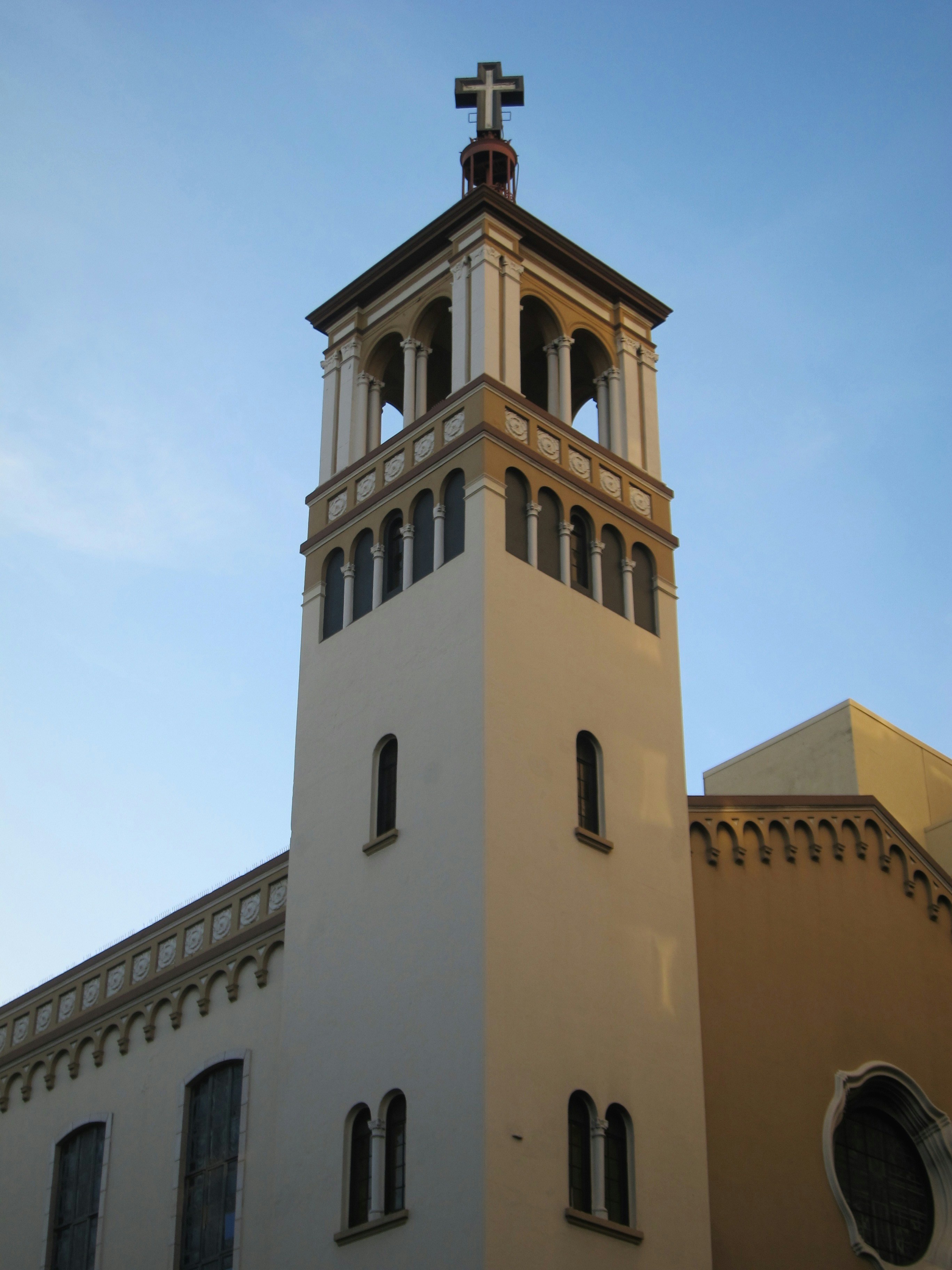 Church bell tower with a prominent cross against a clear blue sky, showcasing architectural details and historical significance.