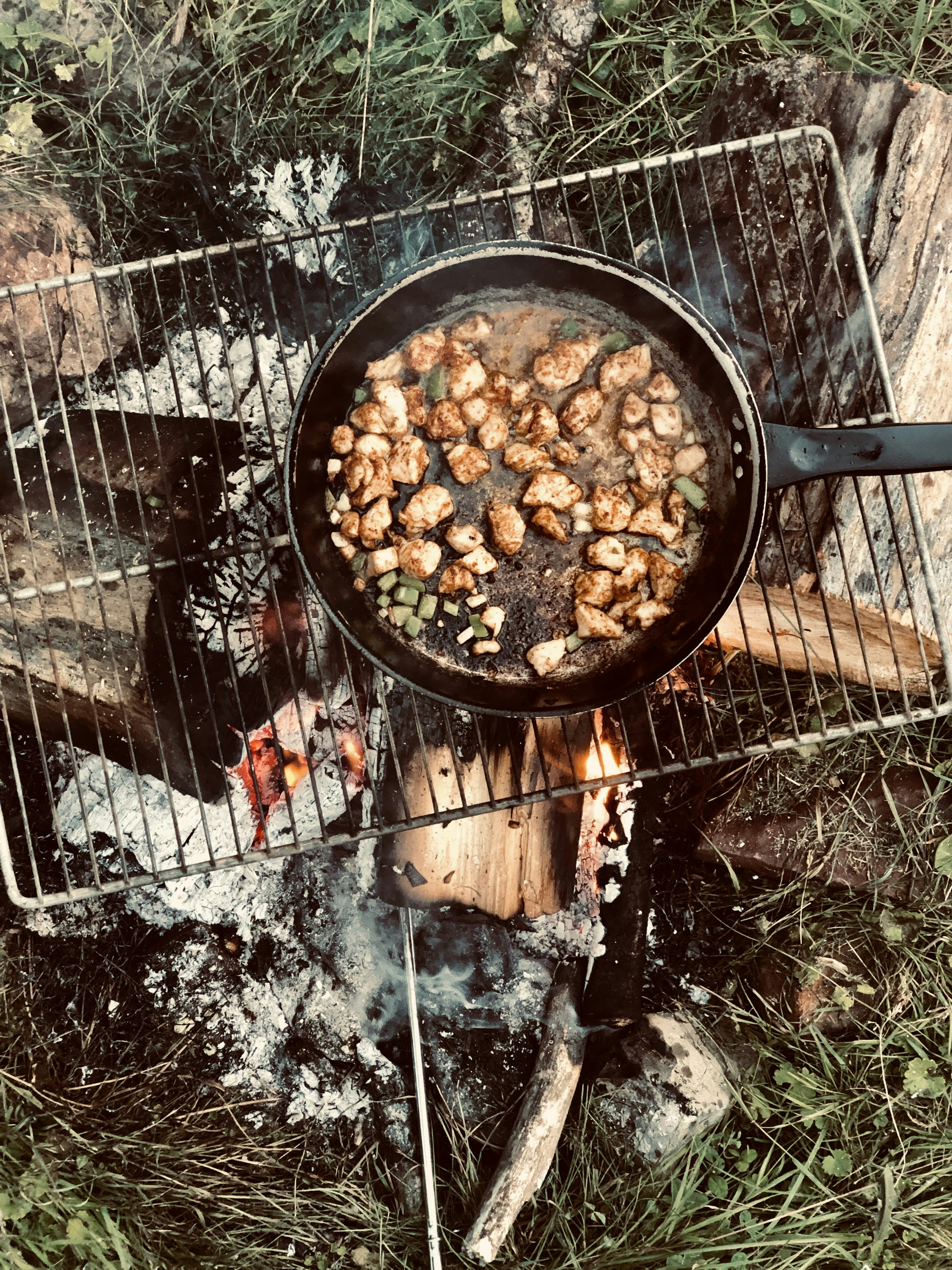 Took this picture of us cooking mountain pies over an open fire, on a cooking grate in a cast iron skillet.  Skillet chicken, peppers, onions, spices, etc all go into mountain pie maker with some bread and cheese and makes an amazing sandwich! | black frying pan on focus photography