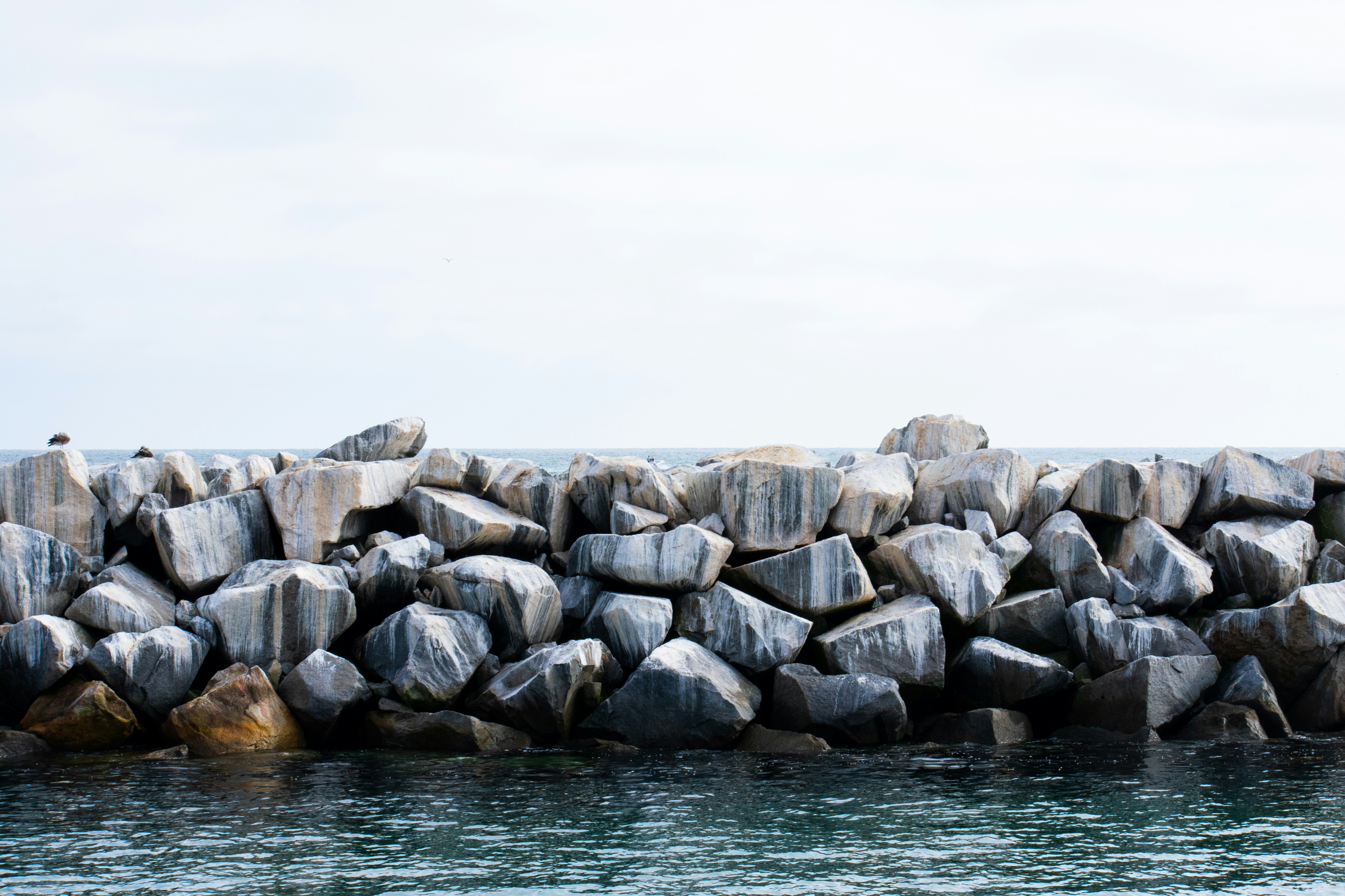 Massive stone breakwater lining a tranquil sea under a cloudy sky.