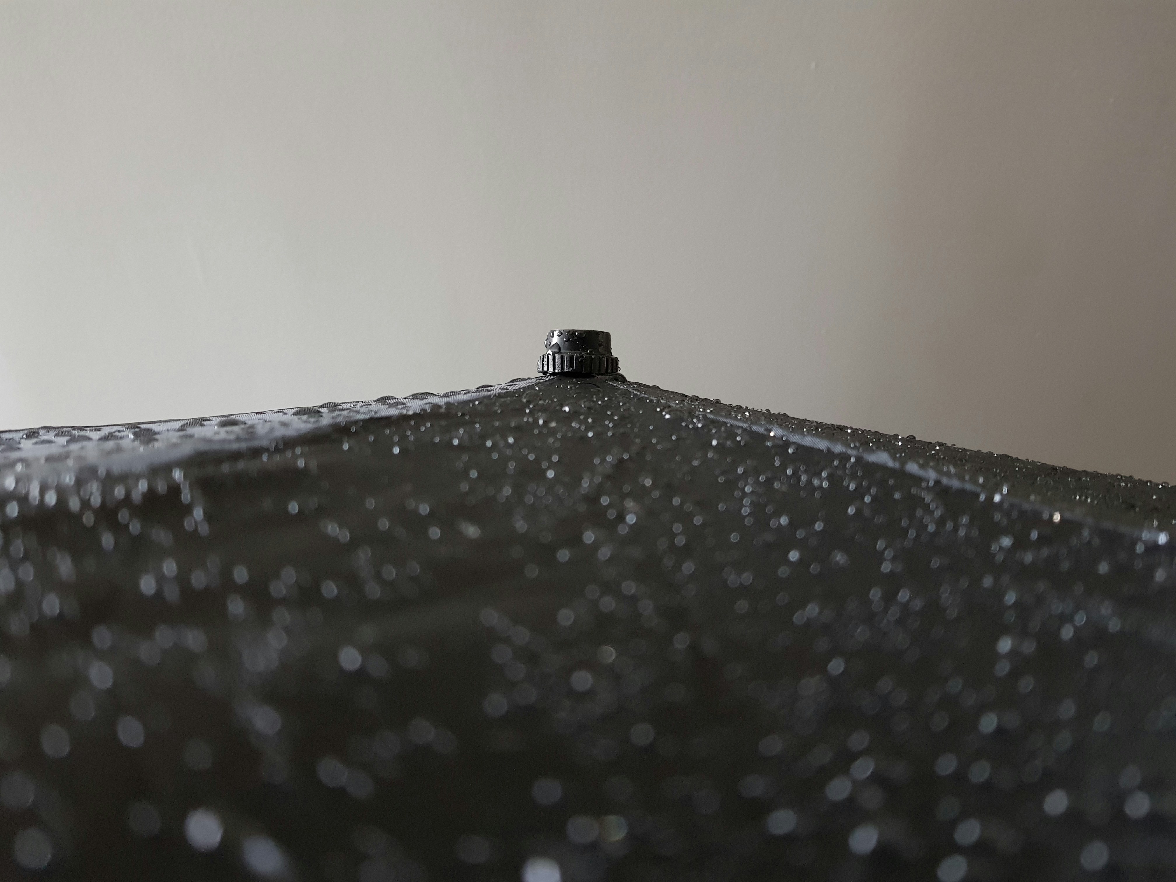 Close-up view of droplets resting on a black umbrella, showcasing the interplay of light and texture against a neutral background.