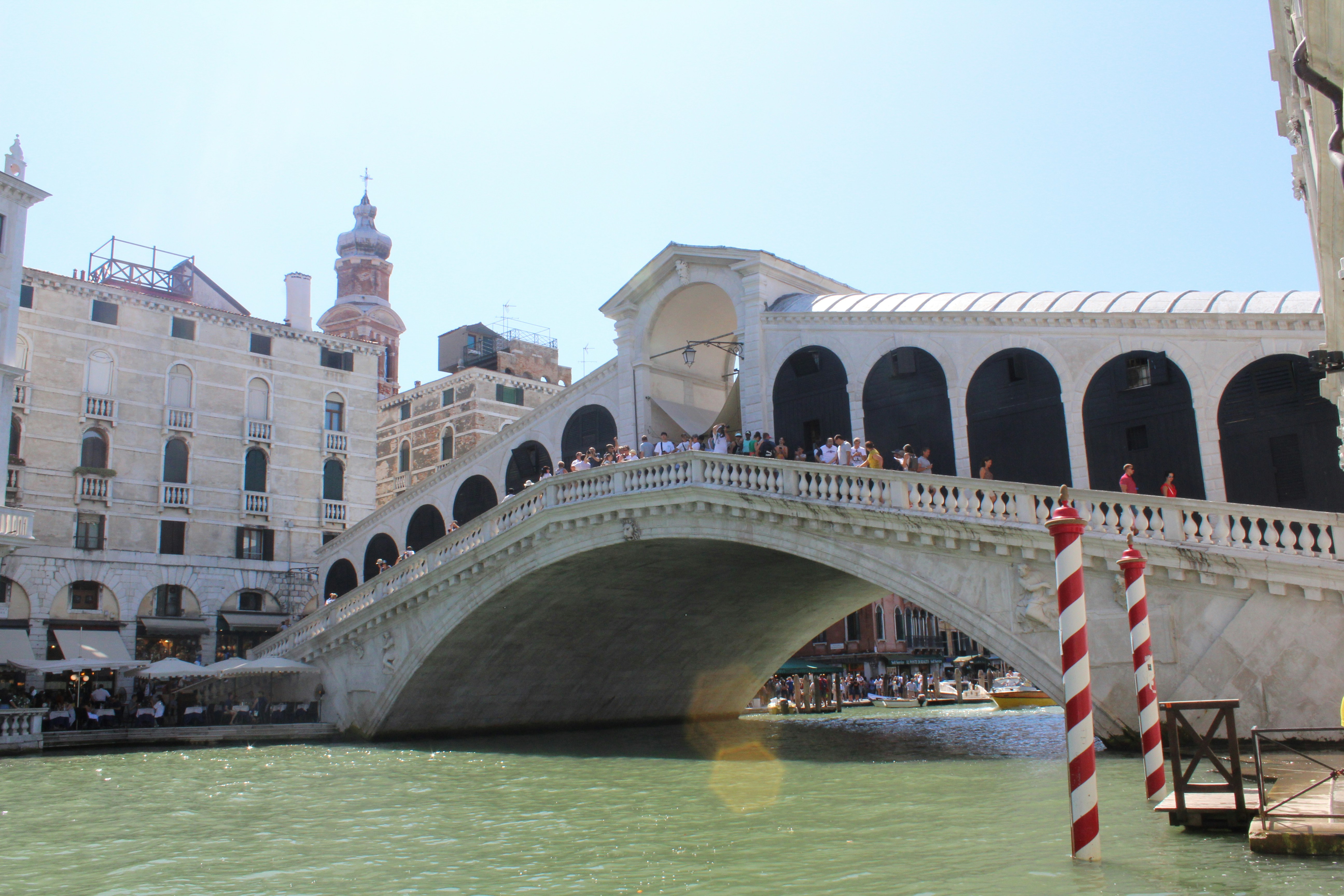 Historic stone bridge spans a bustling canal under a clear blue sky.
