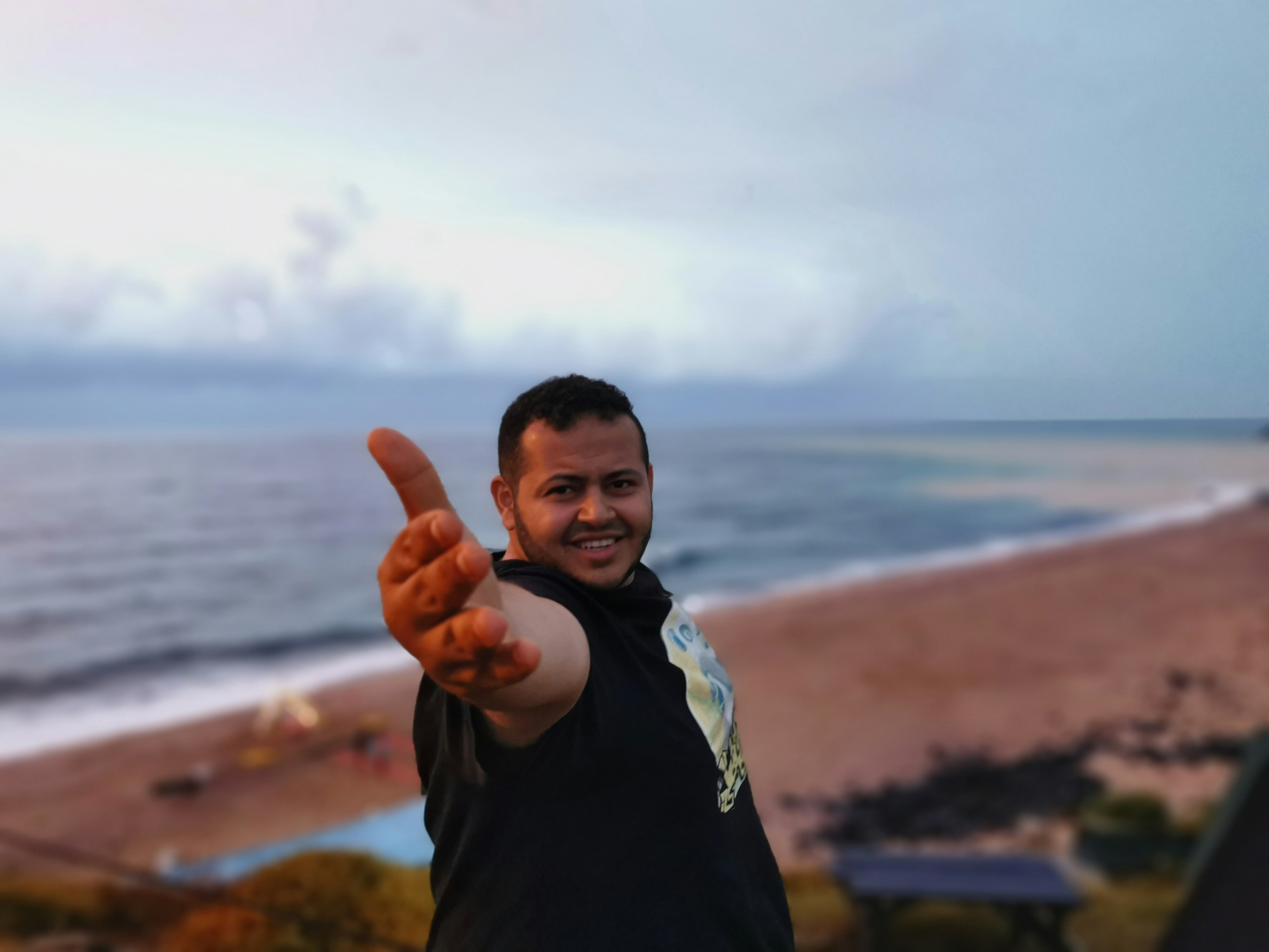 Person extending a hand towards the camera with a blurred beach and ocean in the background.