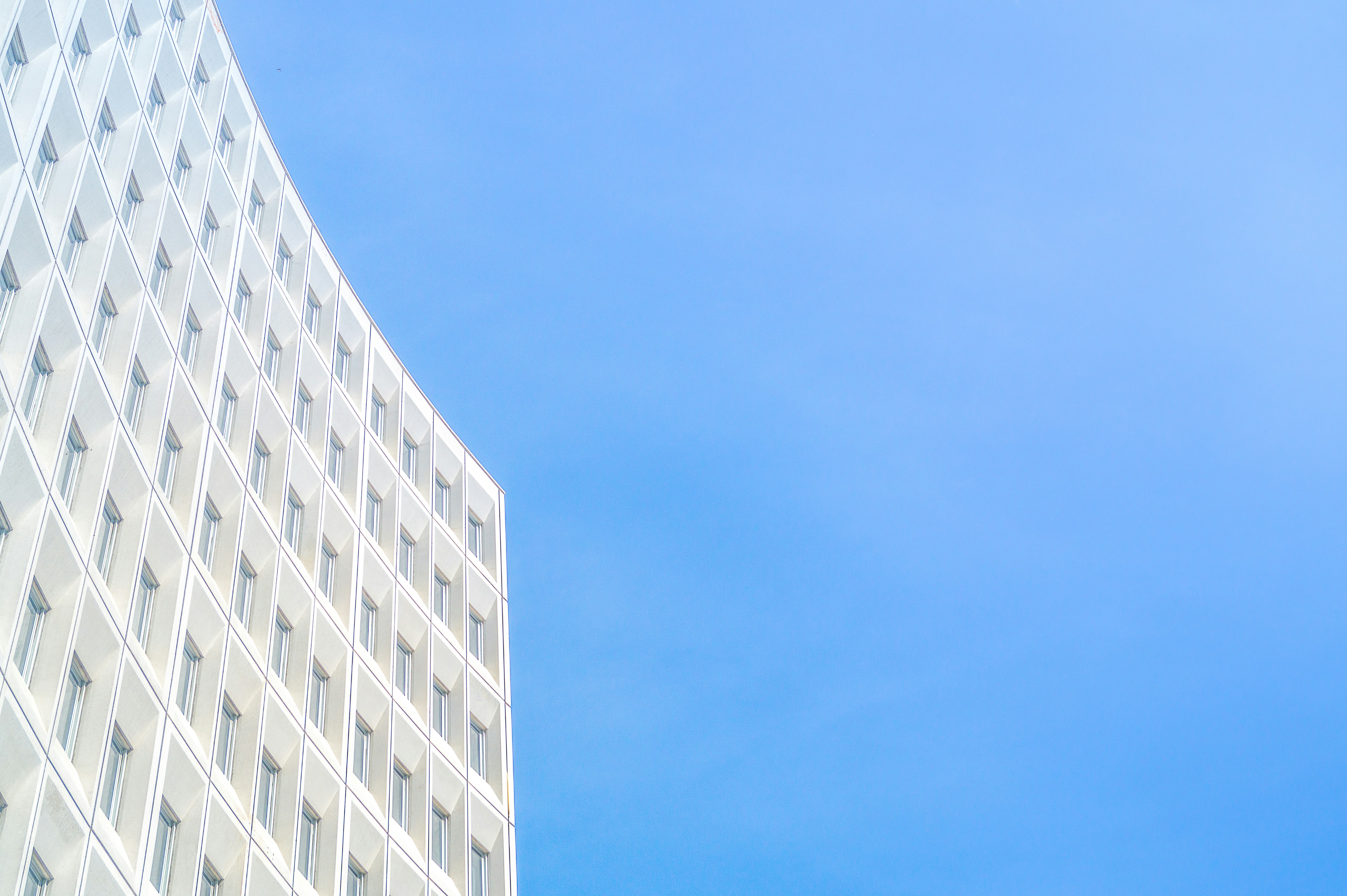 Curved white cement building facade juxtaposed with a clear blue sky.