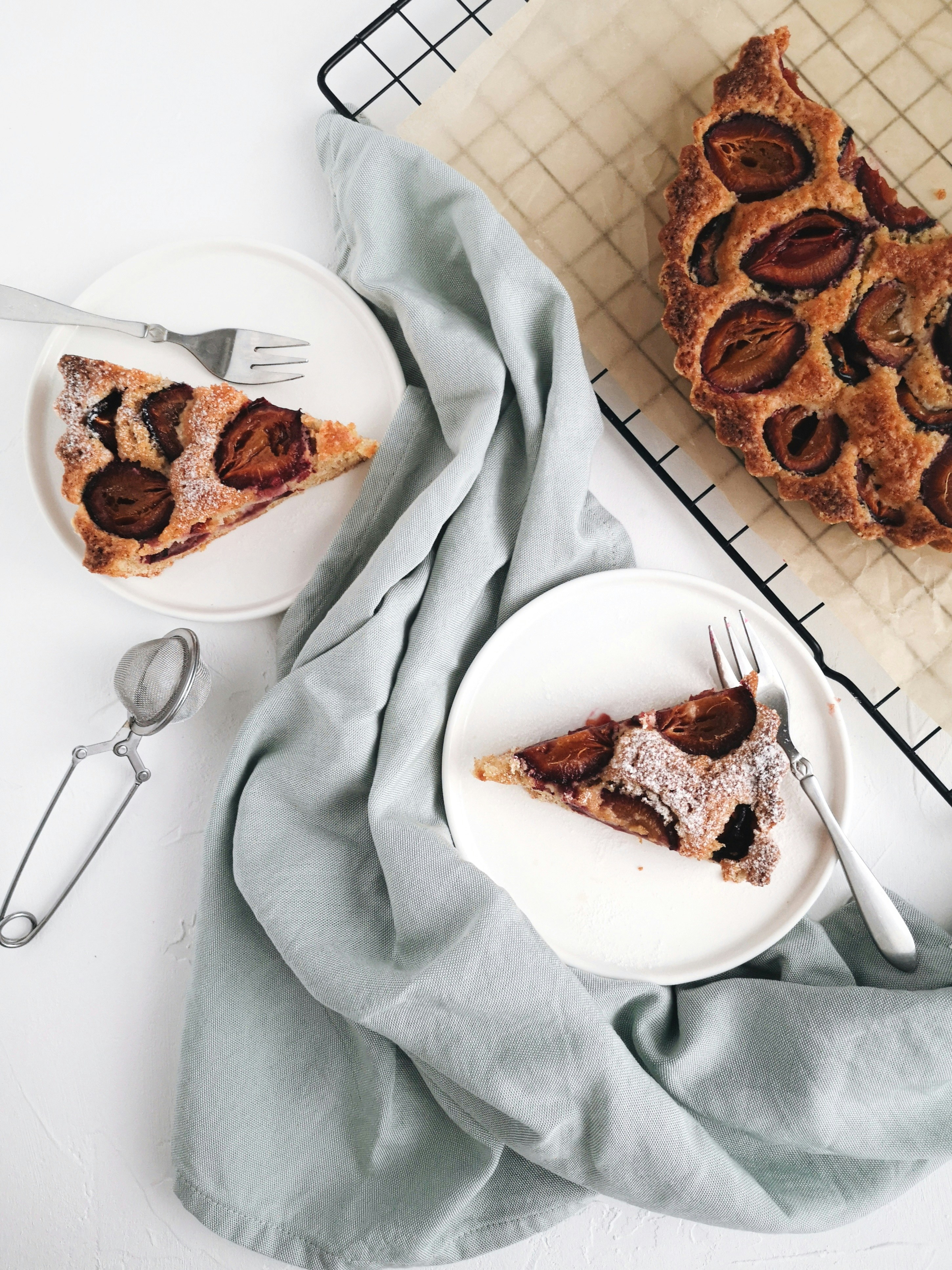 Top-down photograph of a rustic apricot tart with lattice crust, two white plates with slices, set on a pale blue cloth beside a cooling rack.