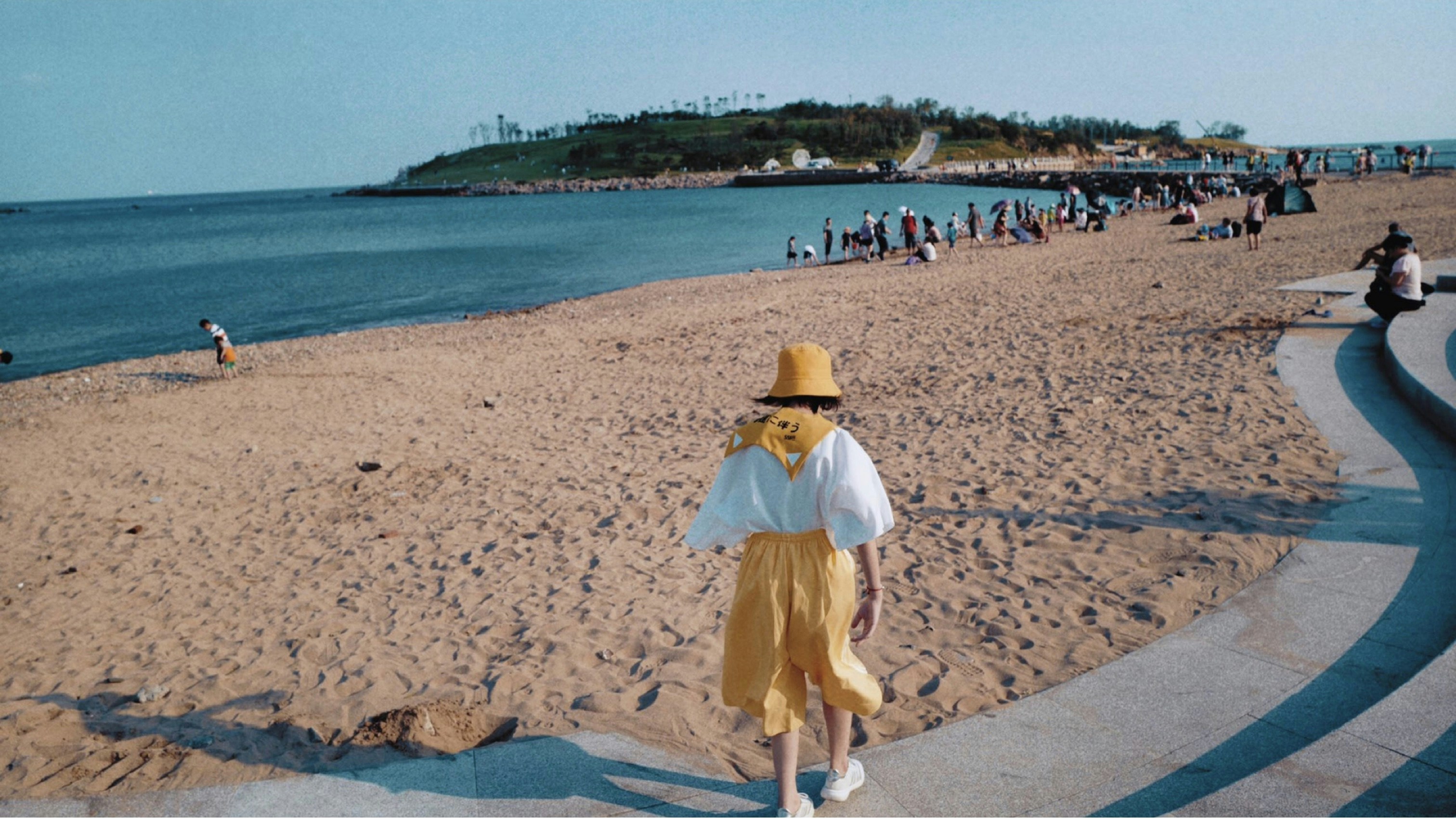 Sunlit promenade: a yellow-clad wanderer on a curving beach path