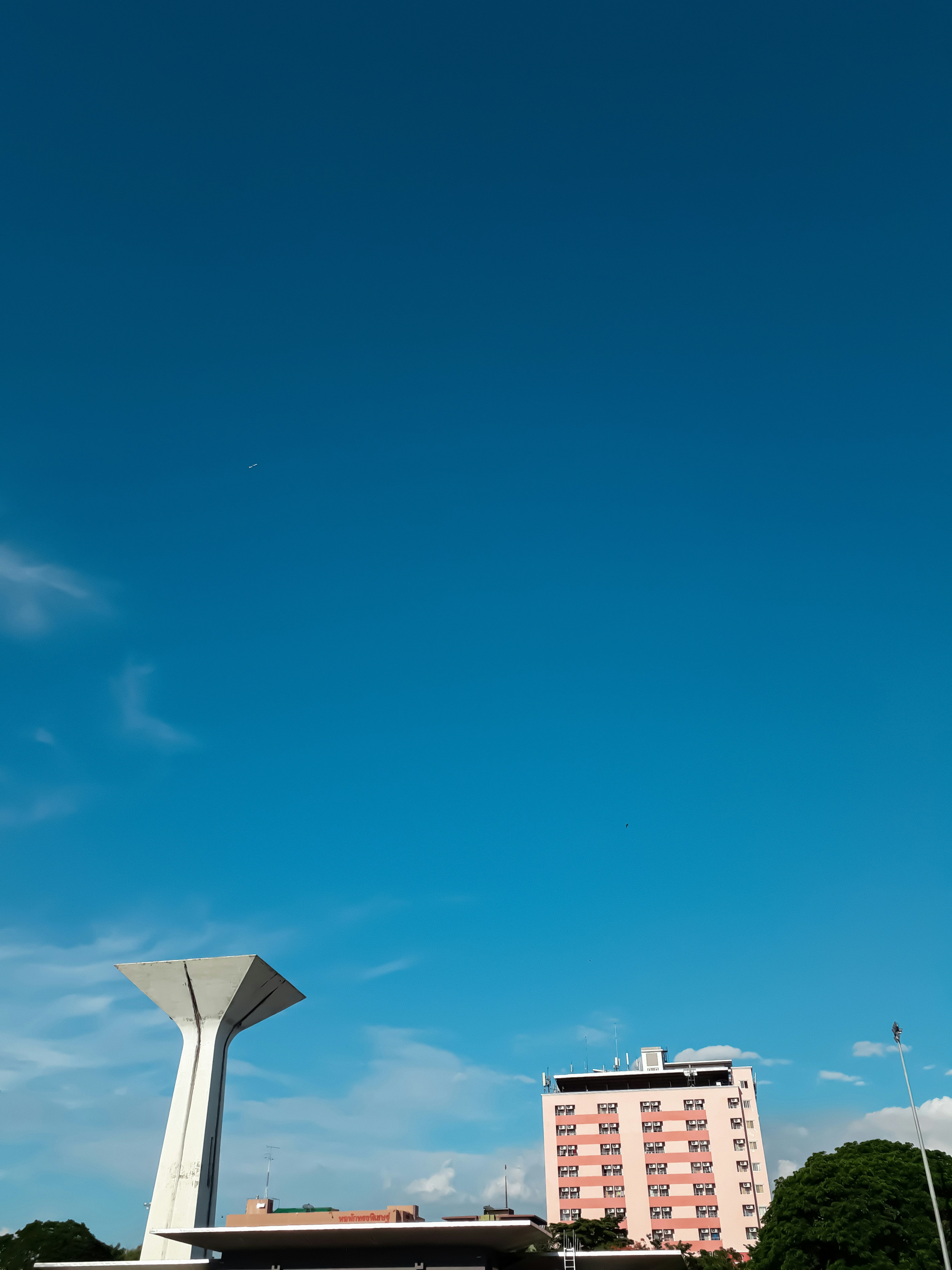 Blue sky dominates the frame with a coral-pink residential building and a sculptural white pillar in the foreground. The image captures urban geometry against a clear day.